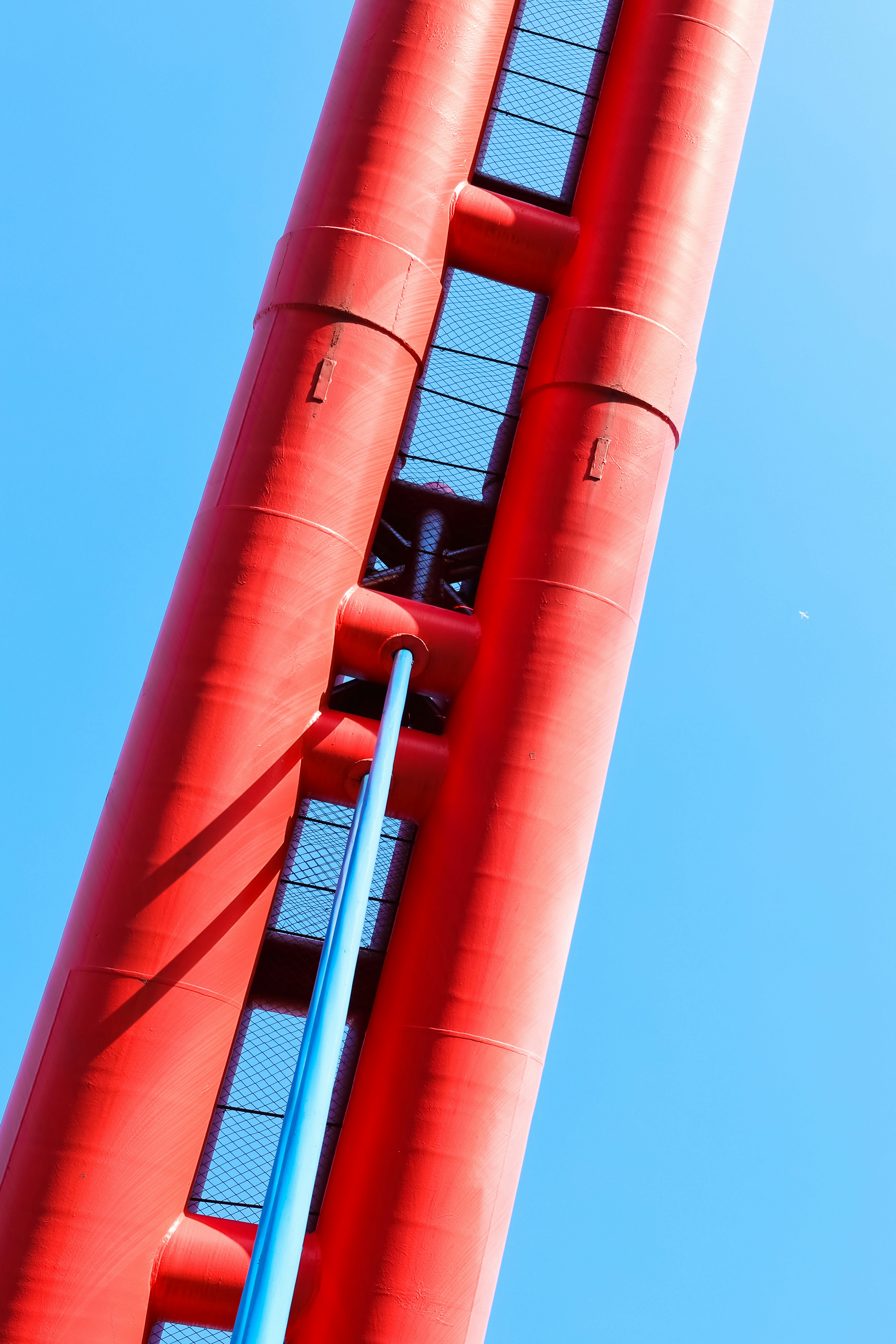 Crimson Pillars Against a Sky: A Blue Rod Traverses a Tilted Red Tower