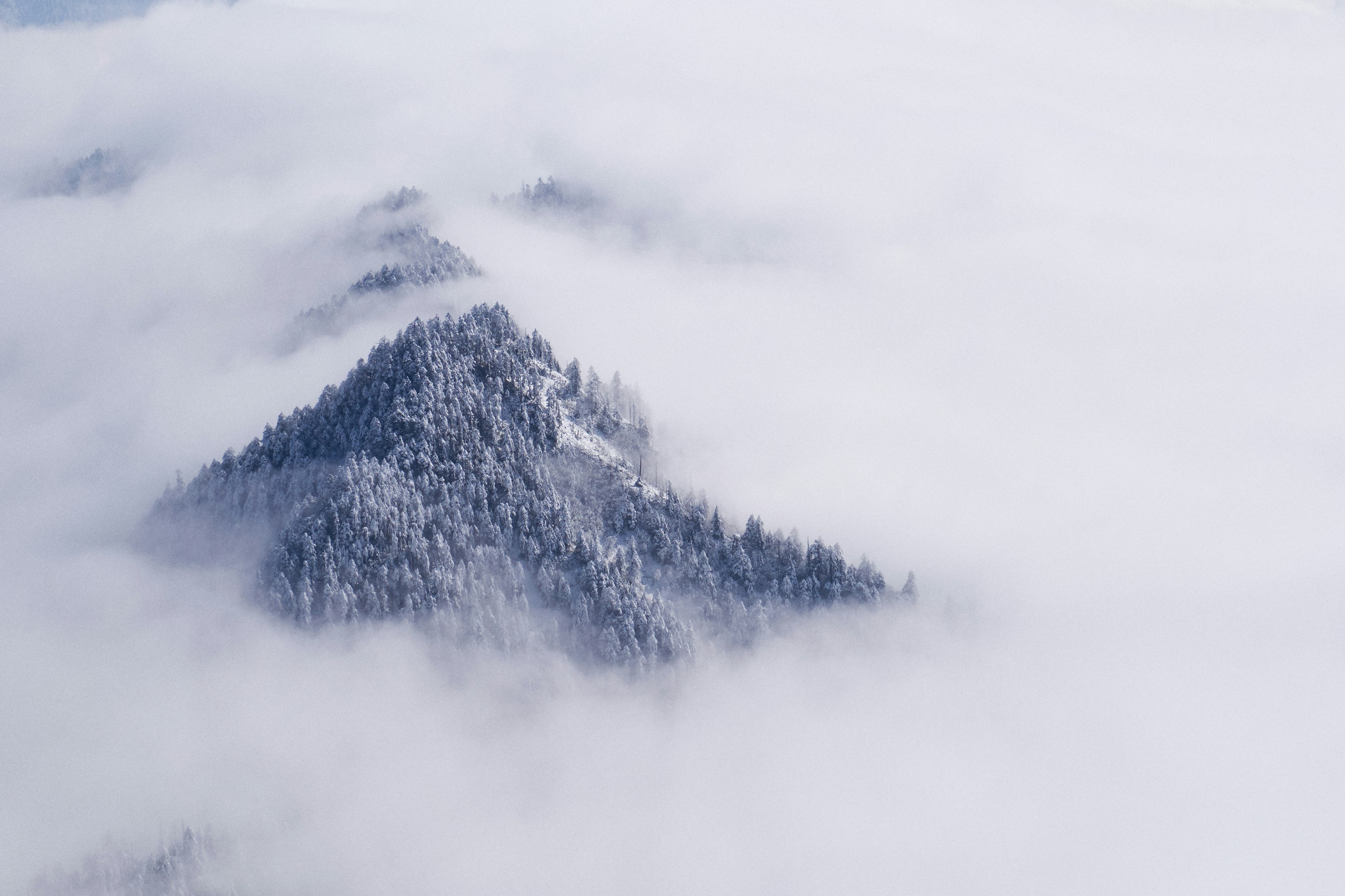 Snow-covered mountain peak emerging through dense clouds.