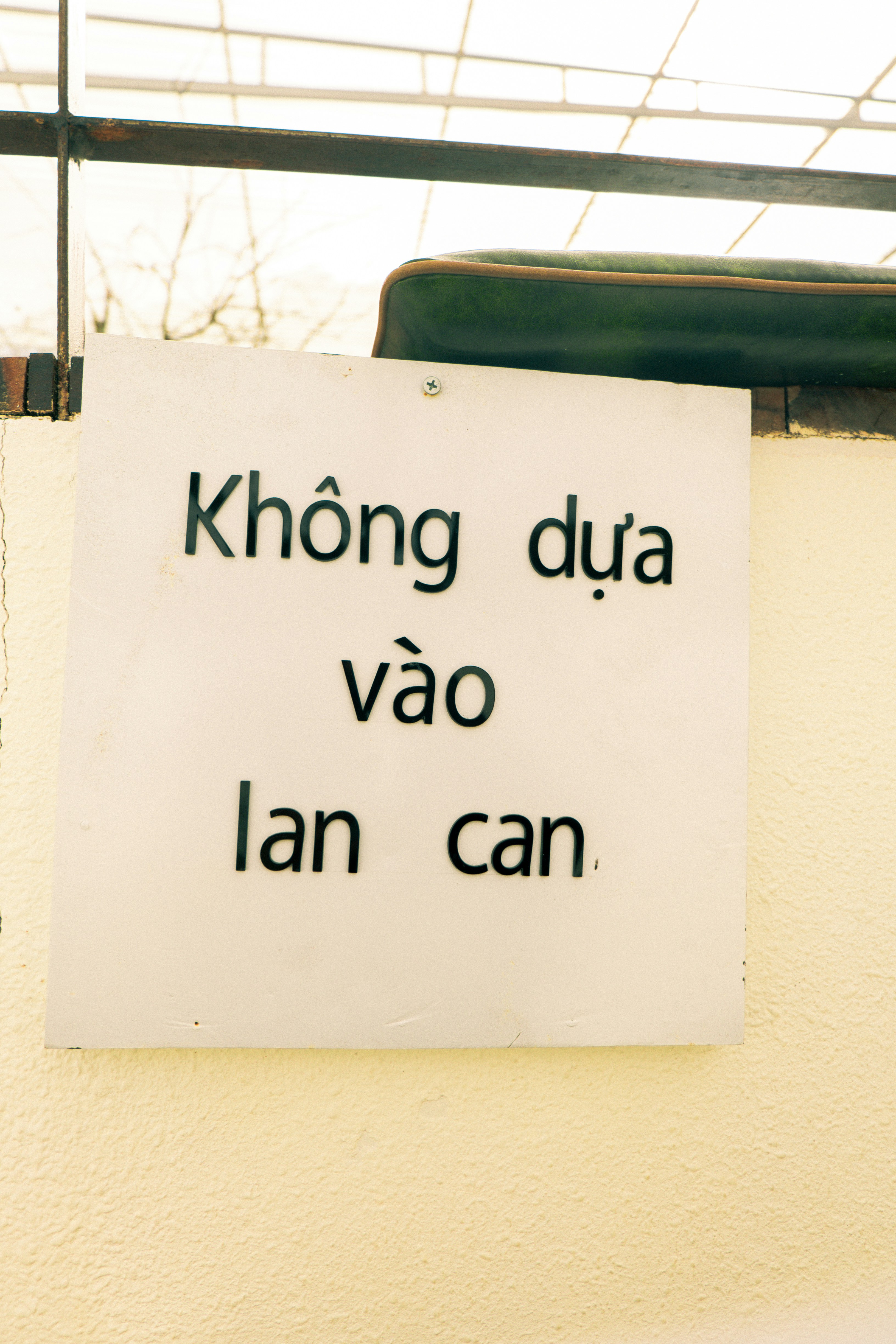 Sign advising against leaning on the railing, featuring bold typography on a simple background.