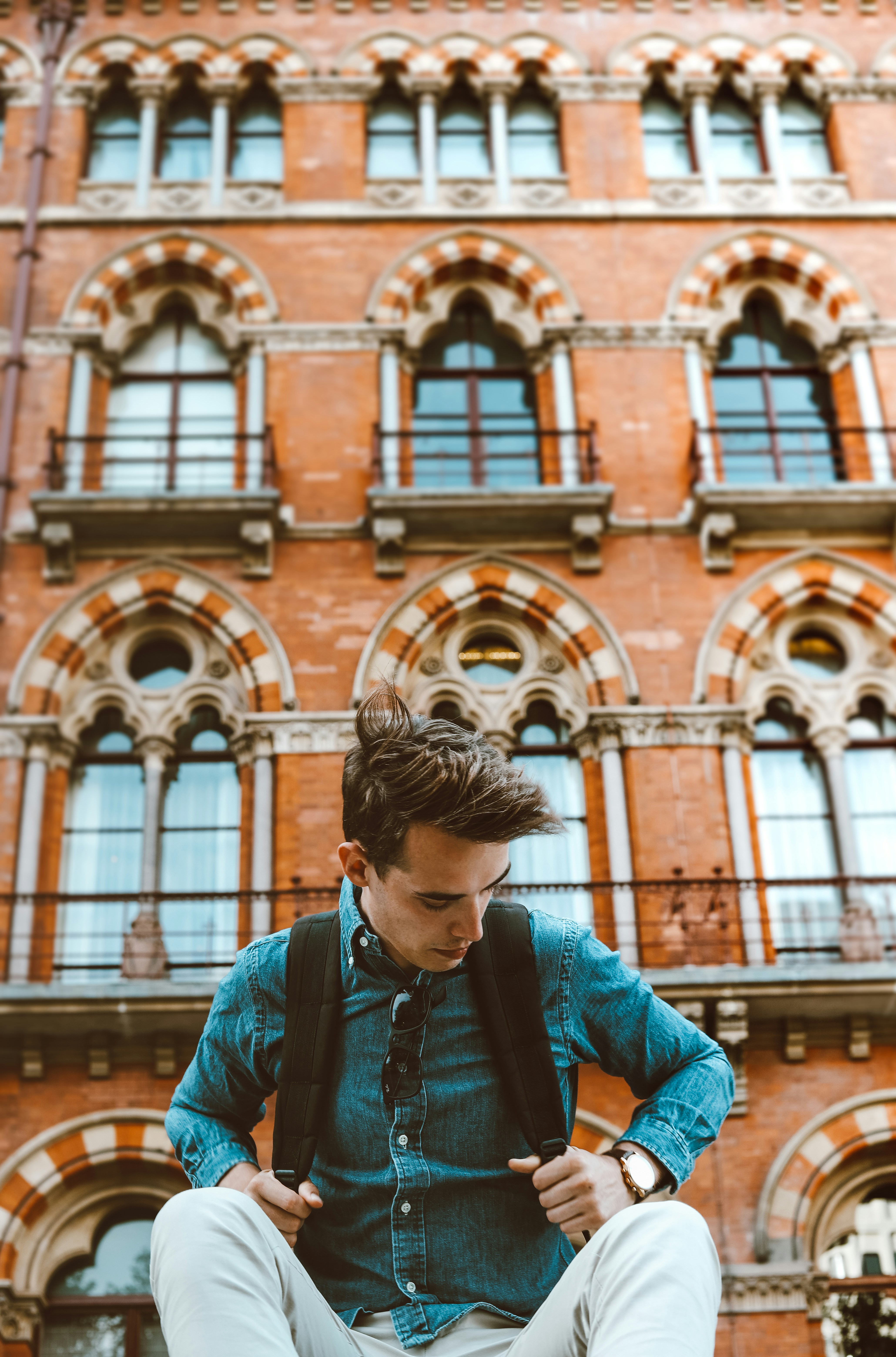 A man sitting on a ledge in front of a building photo – Free Pants ...