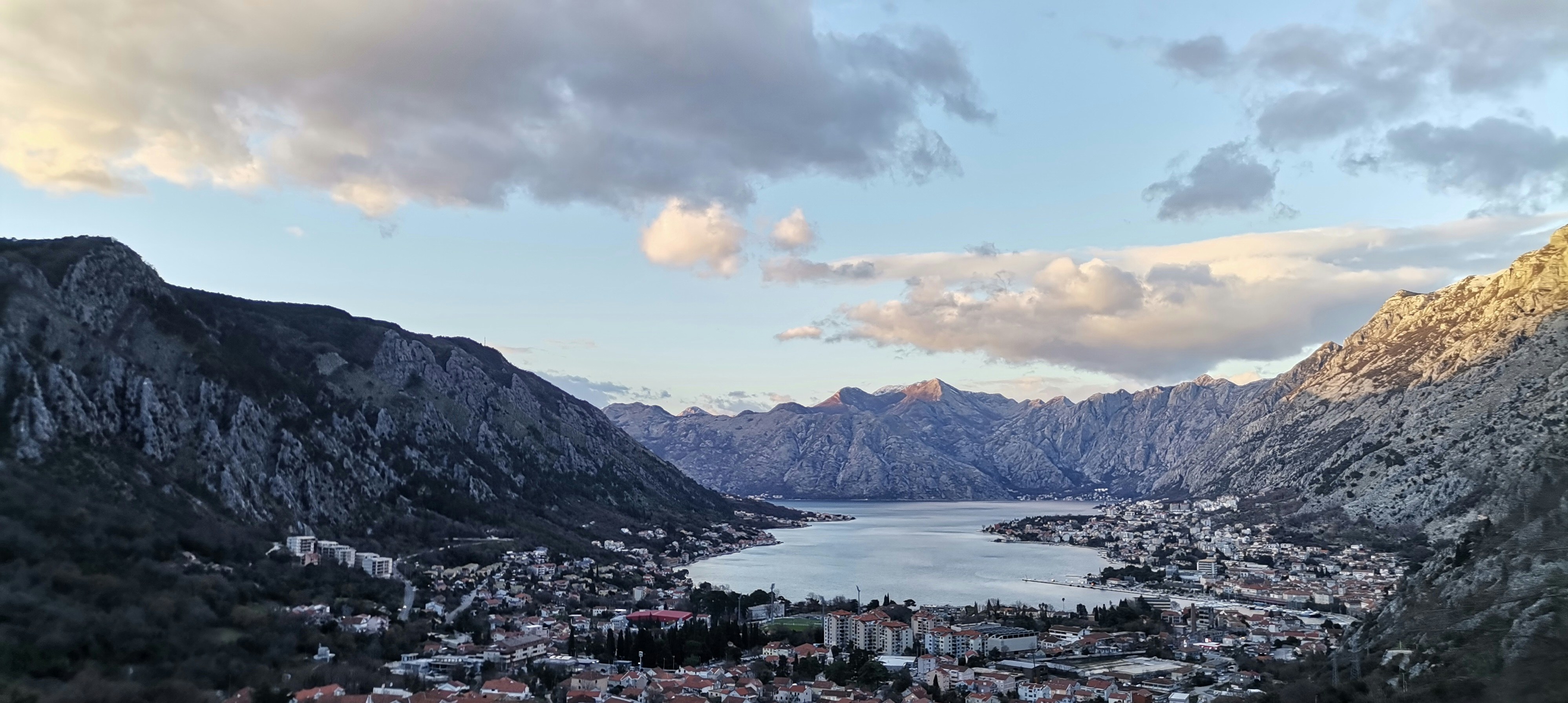 City nestled between rugged mountains and a serene bay under a cloud-dappled sky.