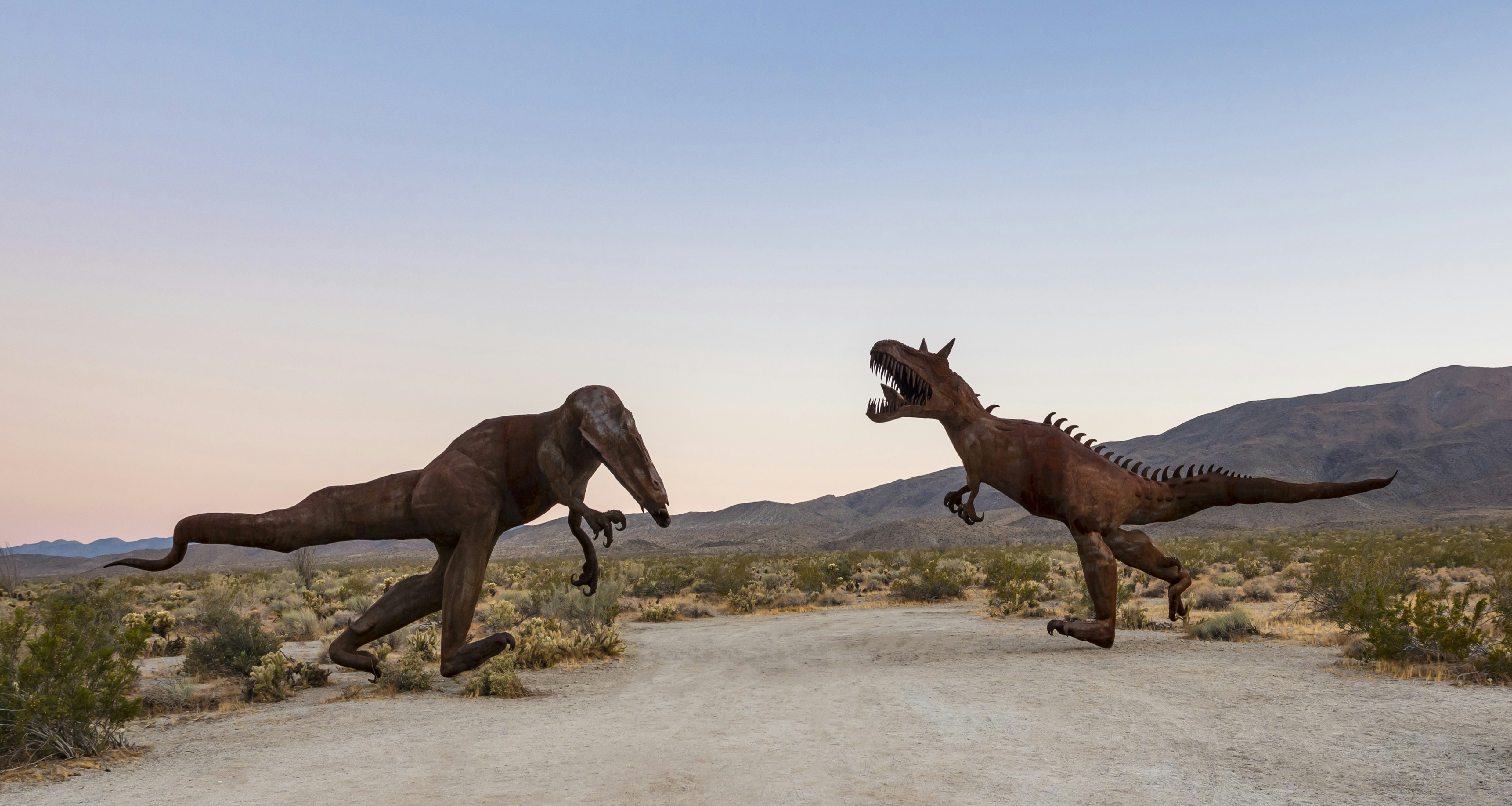 a couple of large dinosaurs standing on top of a dirt road