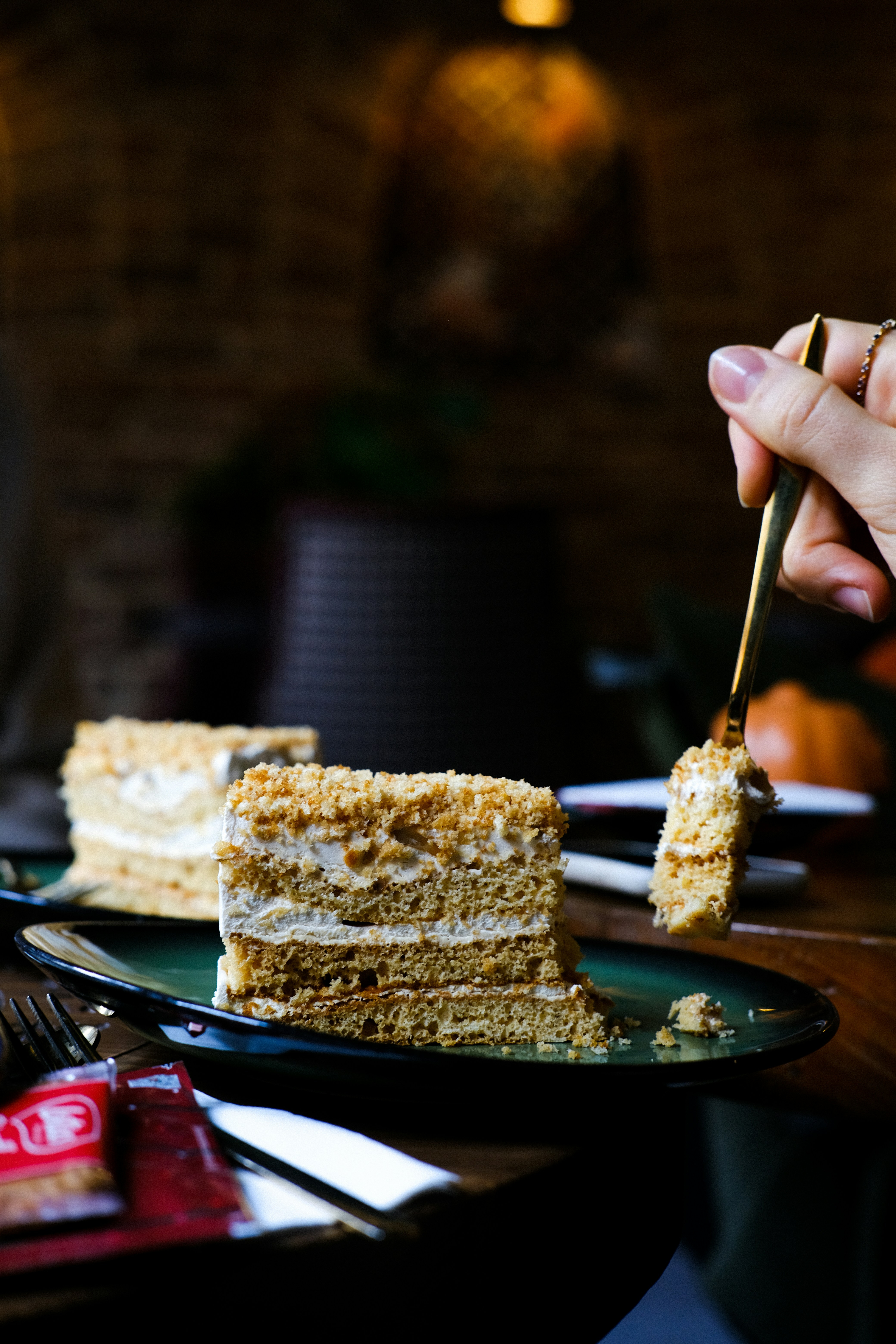 Slice of Creamy Indulgence: A fork lifts a layered cake at a cozy table
