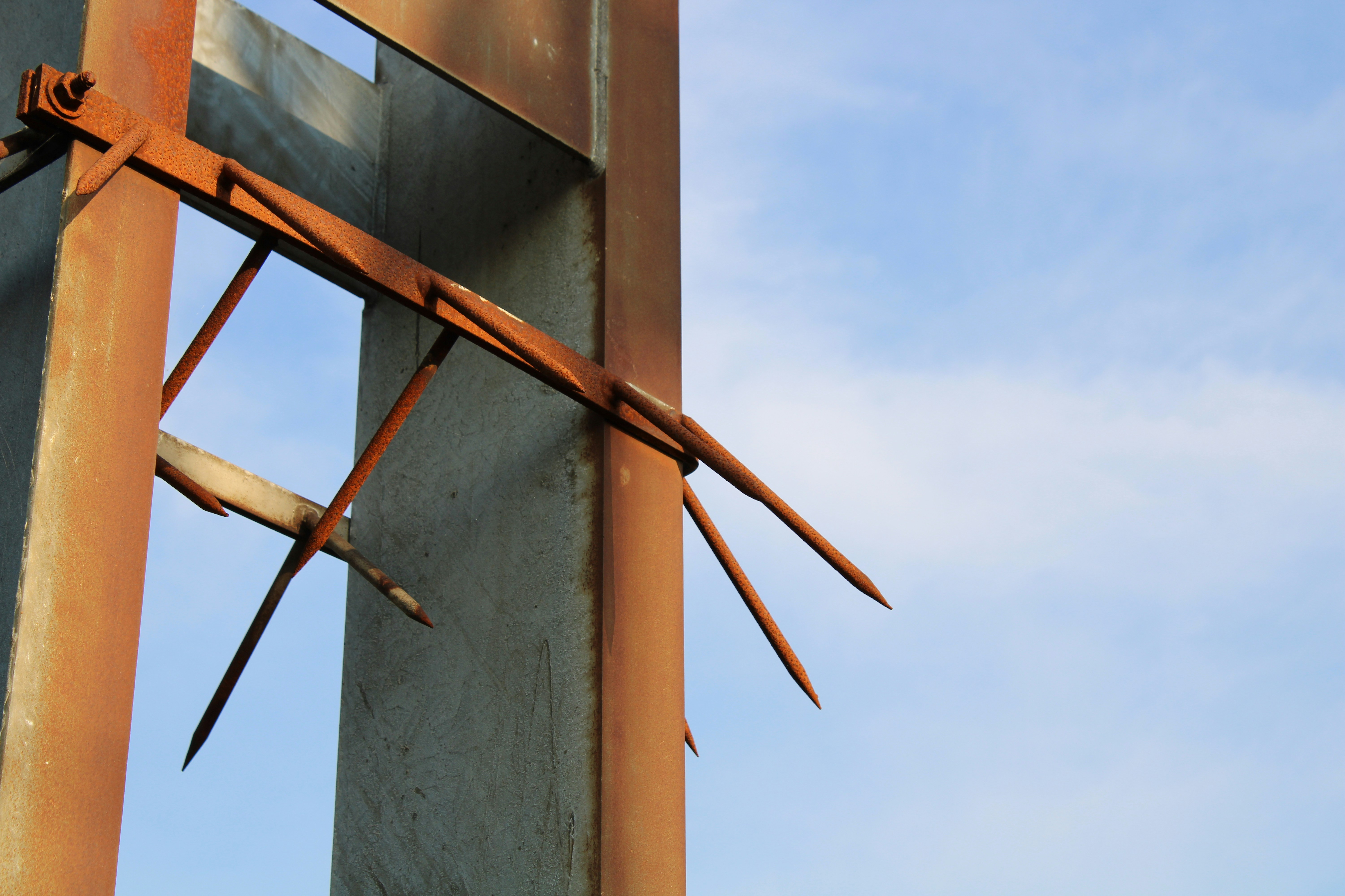 Anti-personal spikes connected to train bridge set against the backdrop of a blue sky with wispy white clouds.