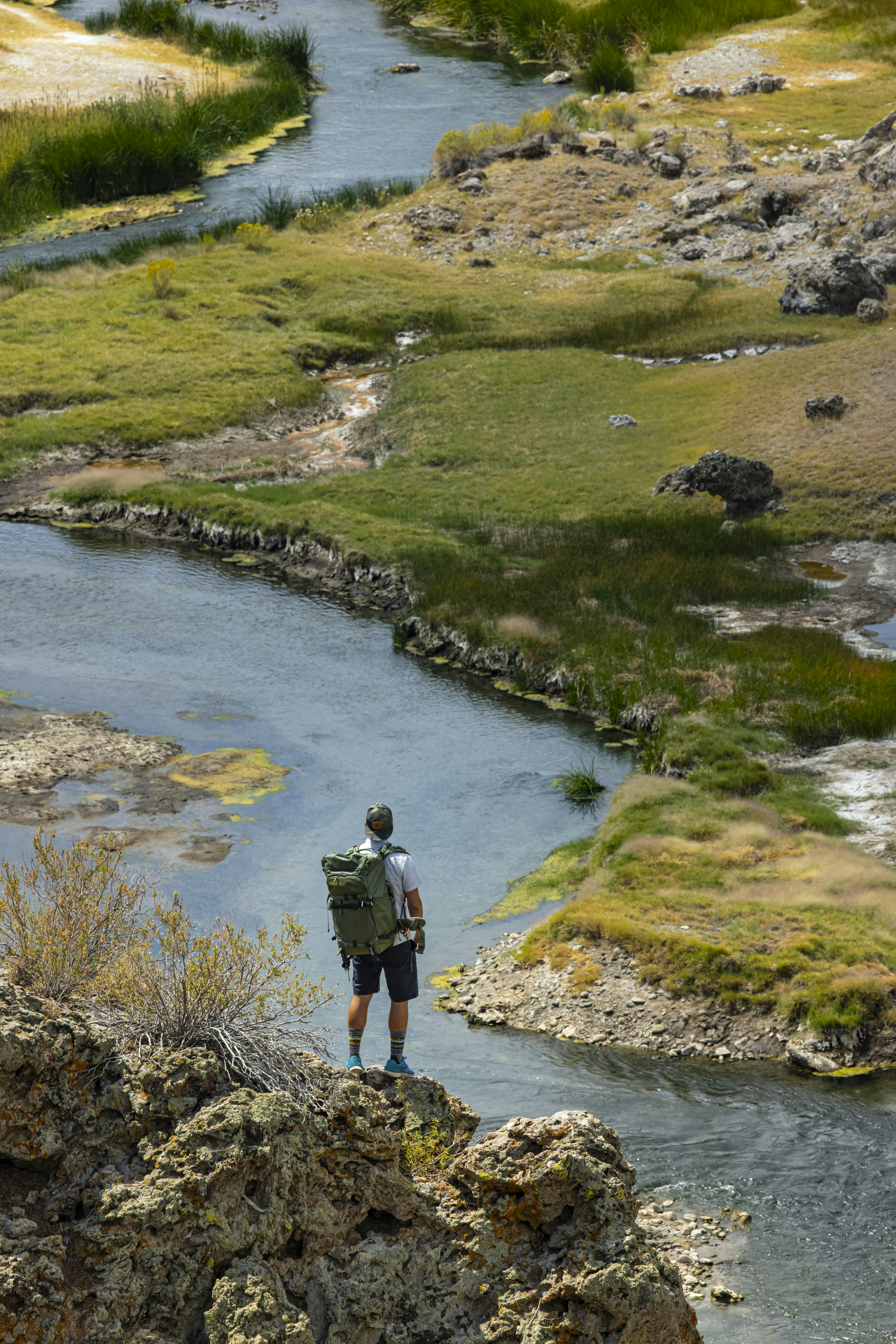 A man with a backpack is standing on a cliff overlooking a river photo ...