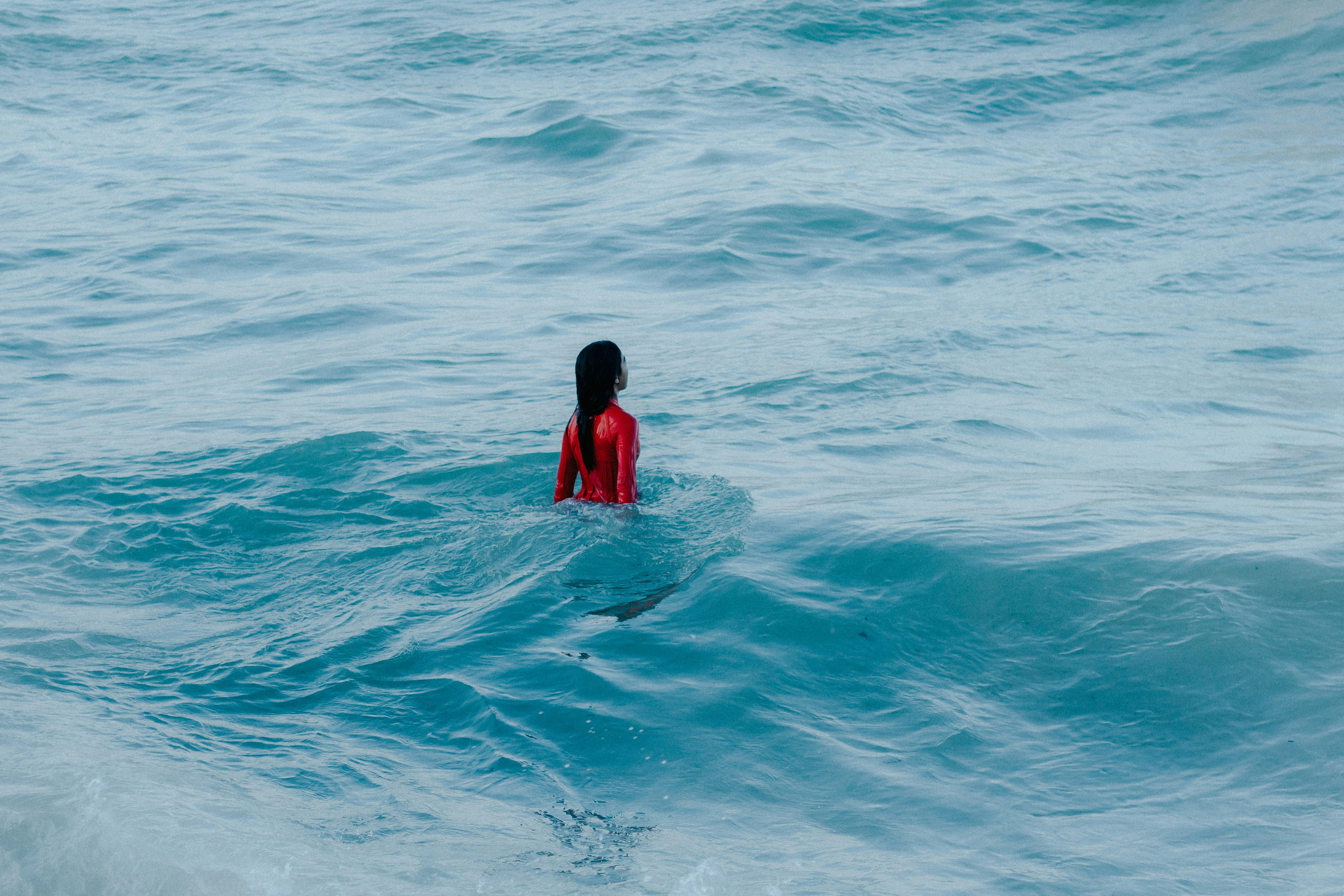 Person in a red shirt immersed in expansive blue ocean waves.