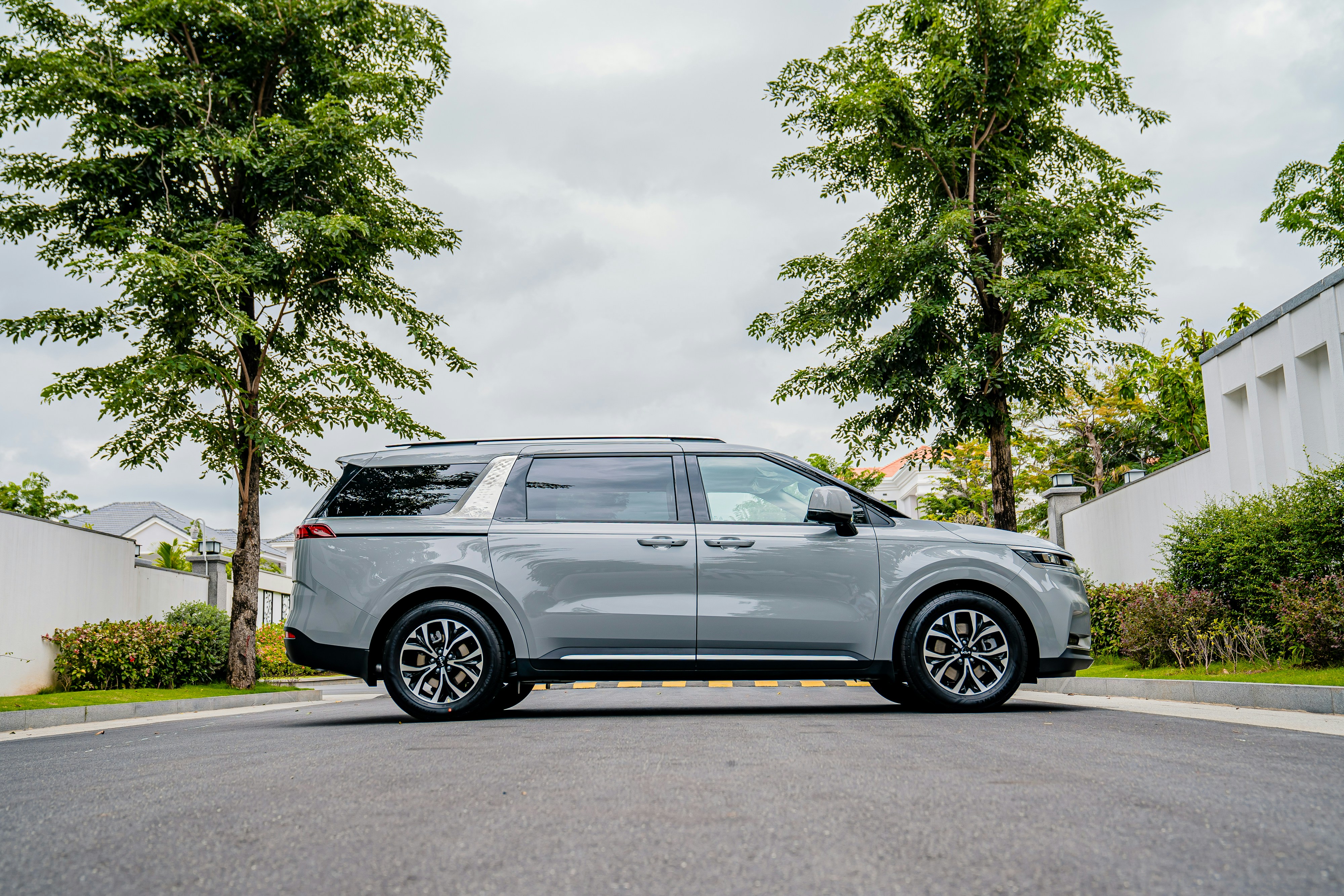 Silver SUV parked on a suburban street flanked by trees and modern buildings under a cloudy sky.