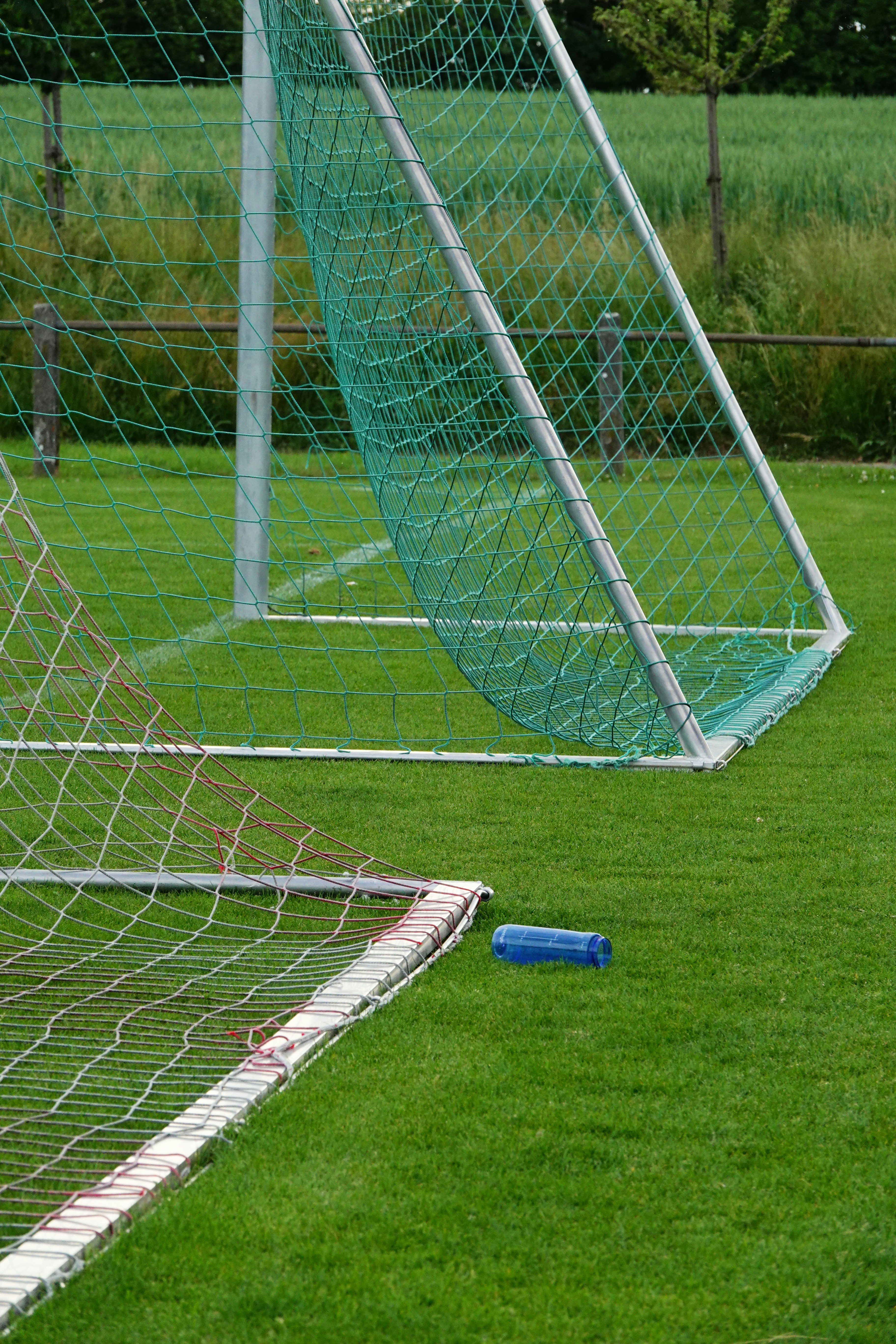 Empty blue water bottle resting on the grass near soccer goalposts on a well-maintained field.