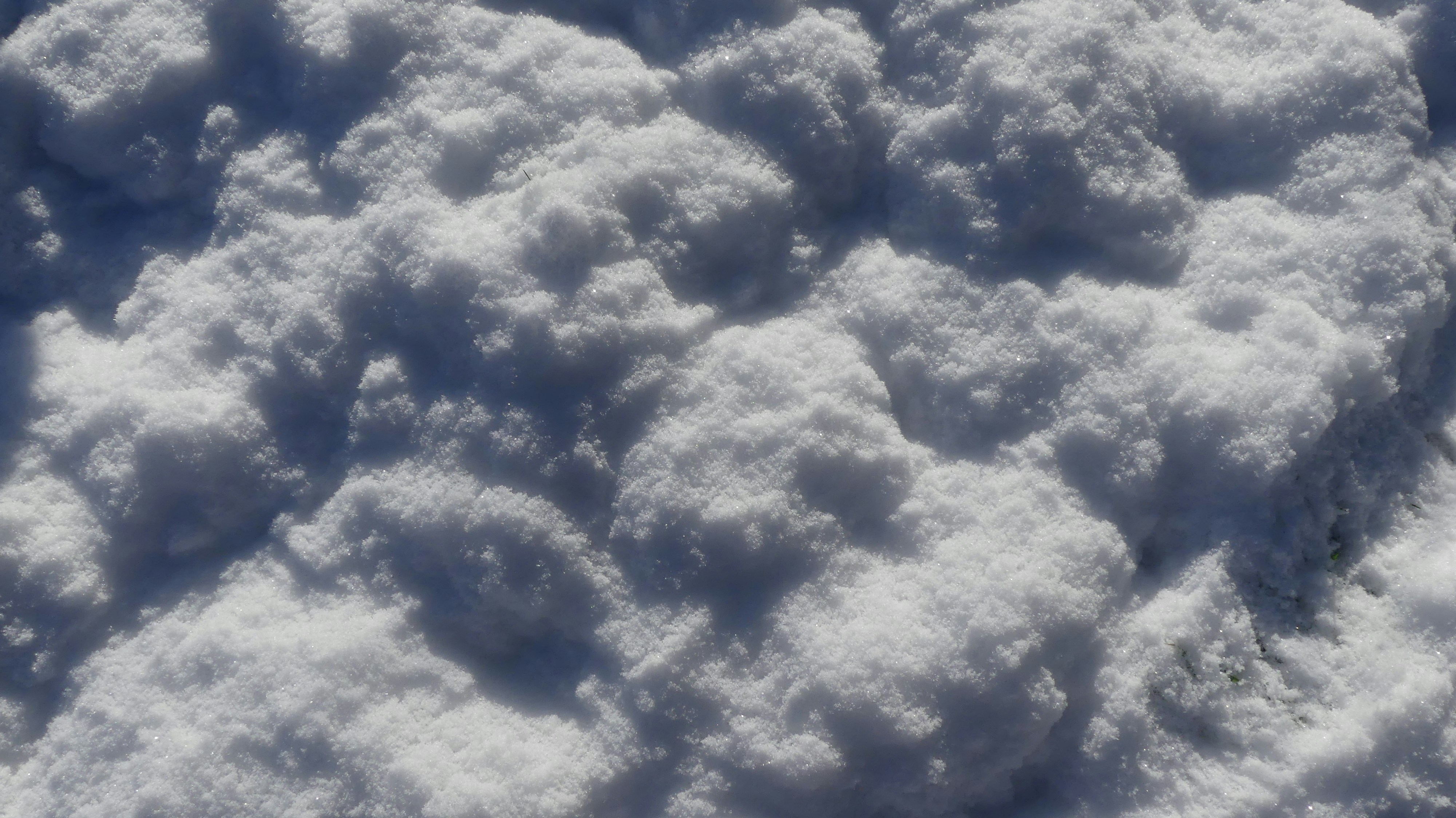 Delicate layers of freshly fallen snow create a soft, textured surface under bright sunlight.