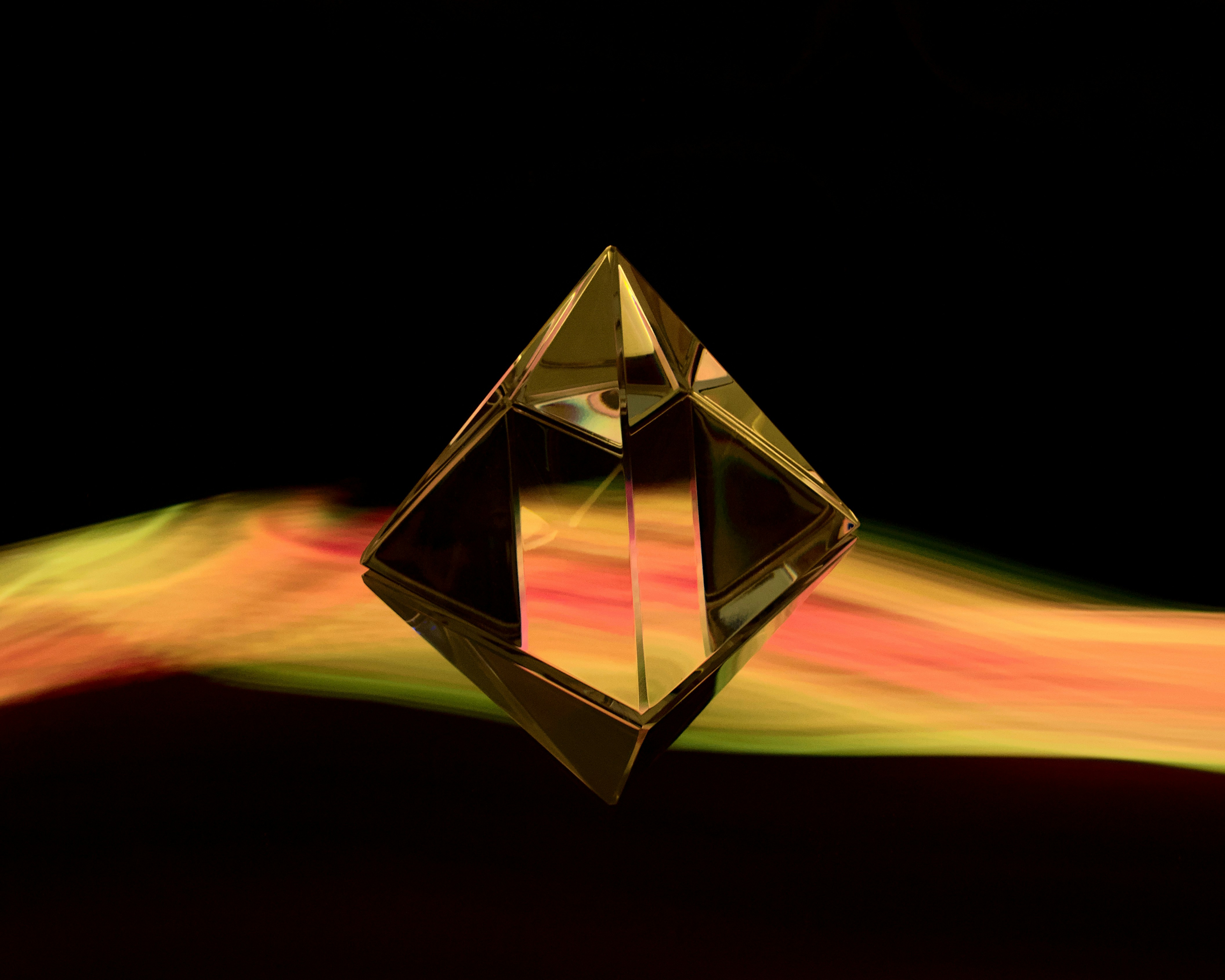 Glass pyramid reflecting vibrant trails of light against a dark background.