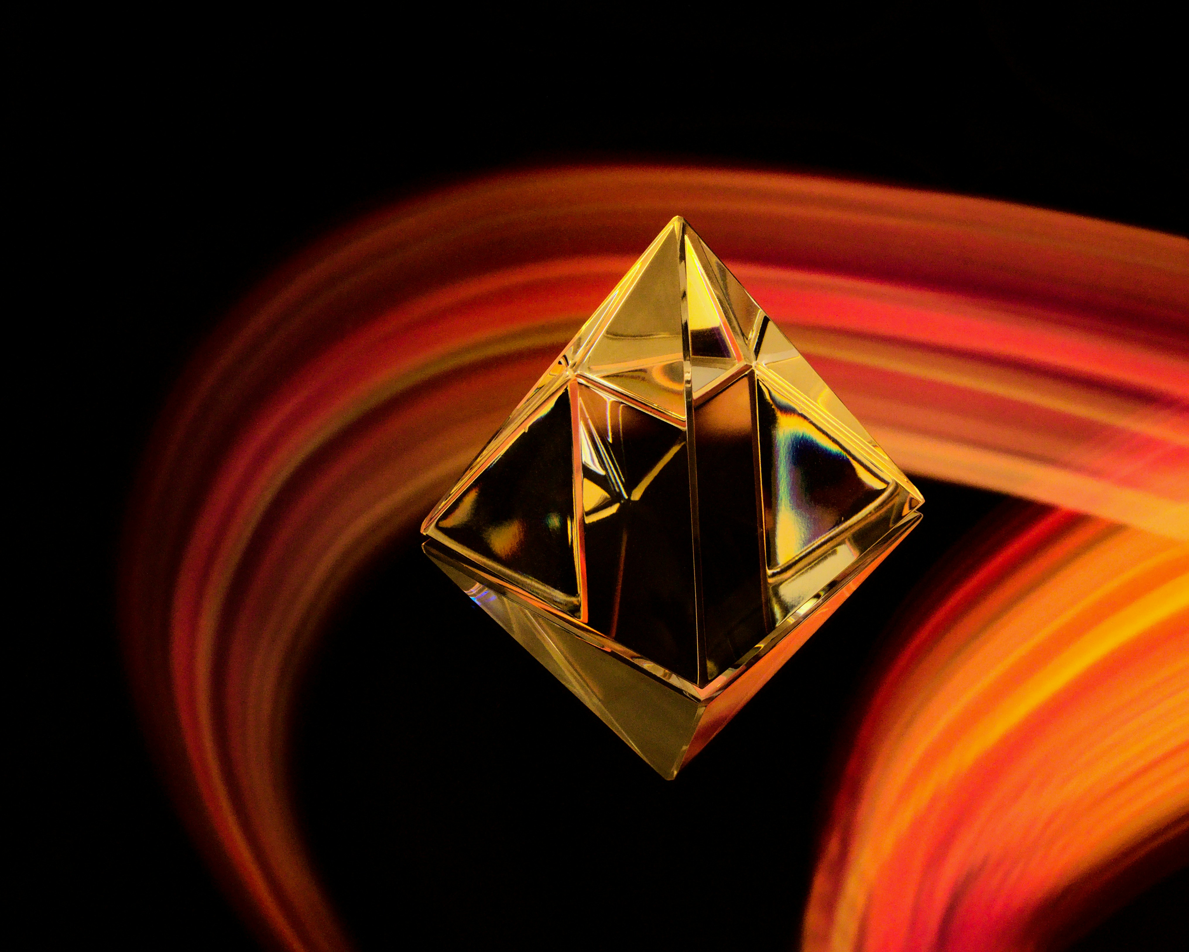 Golden crystal pyramid against swirling red and orange light trails on a black background.
