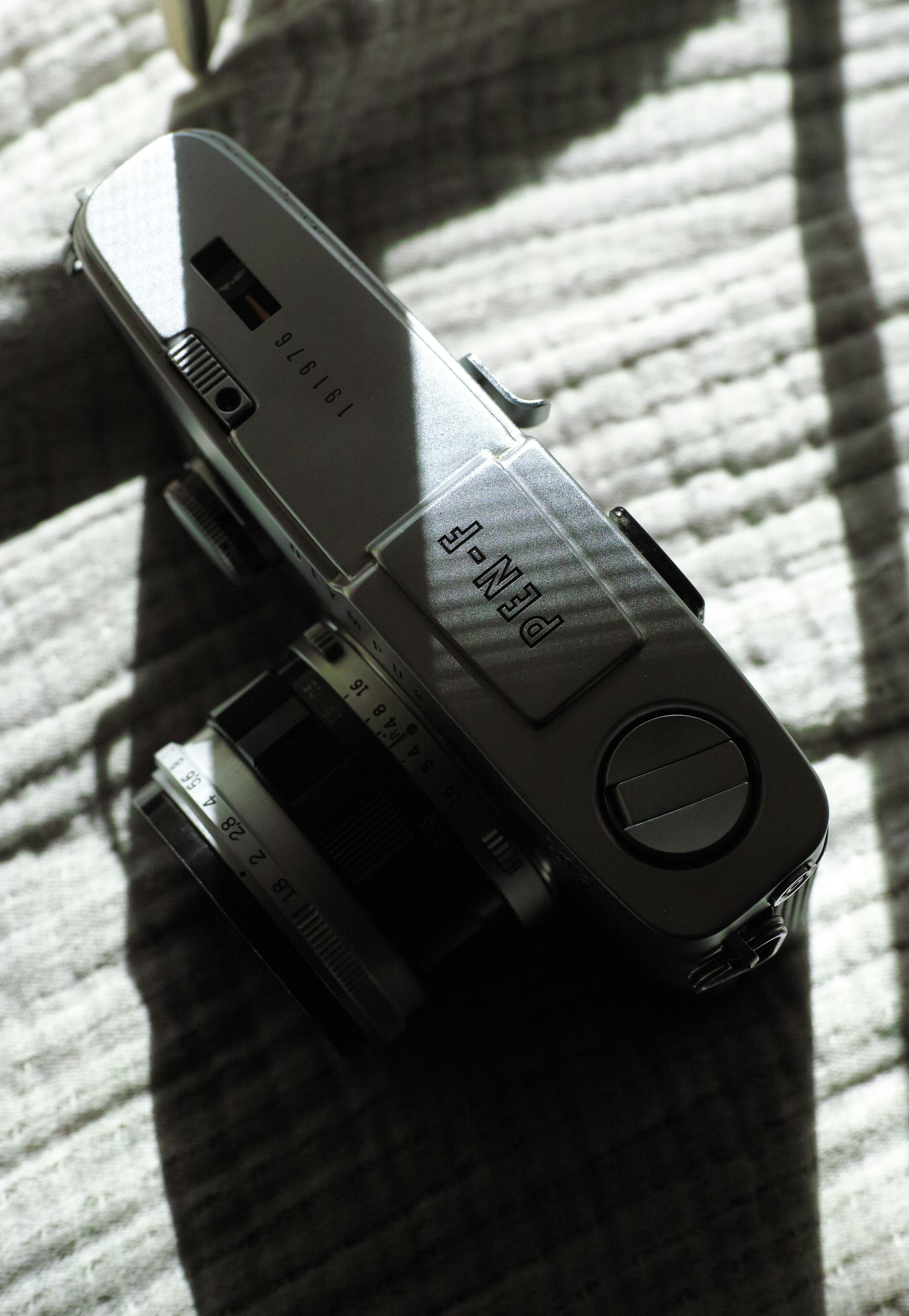 Close-up of a vintage PEN-F camera resting on textured fabric, illuminated by soft natural light.
