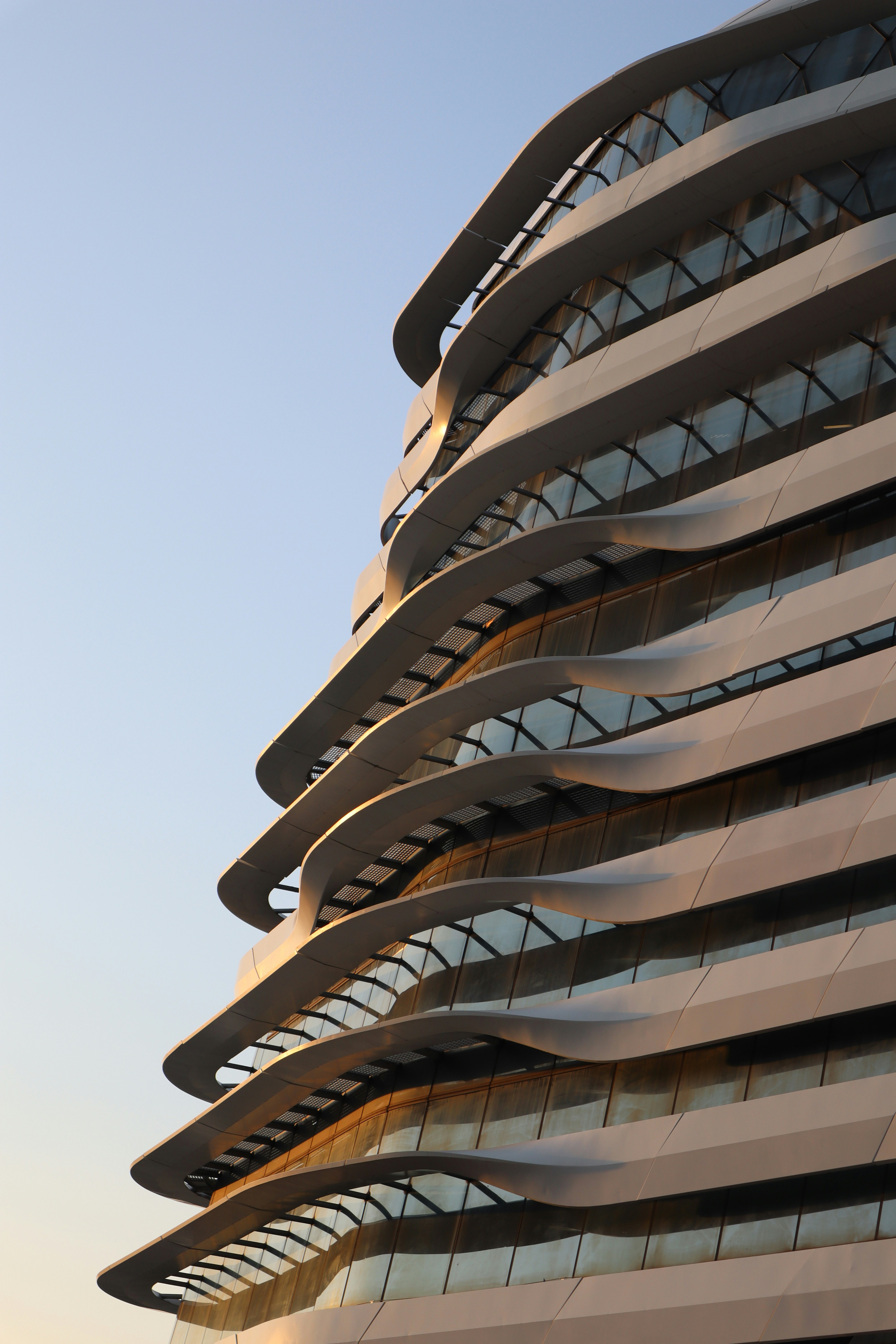 Curvilinear building facade with layered, wave-like elements reflecting soft evening light.