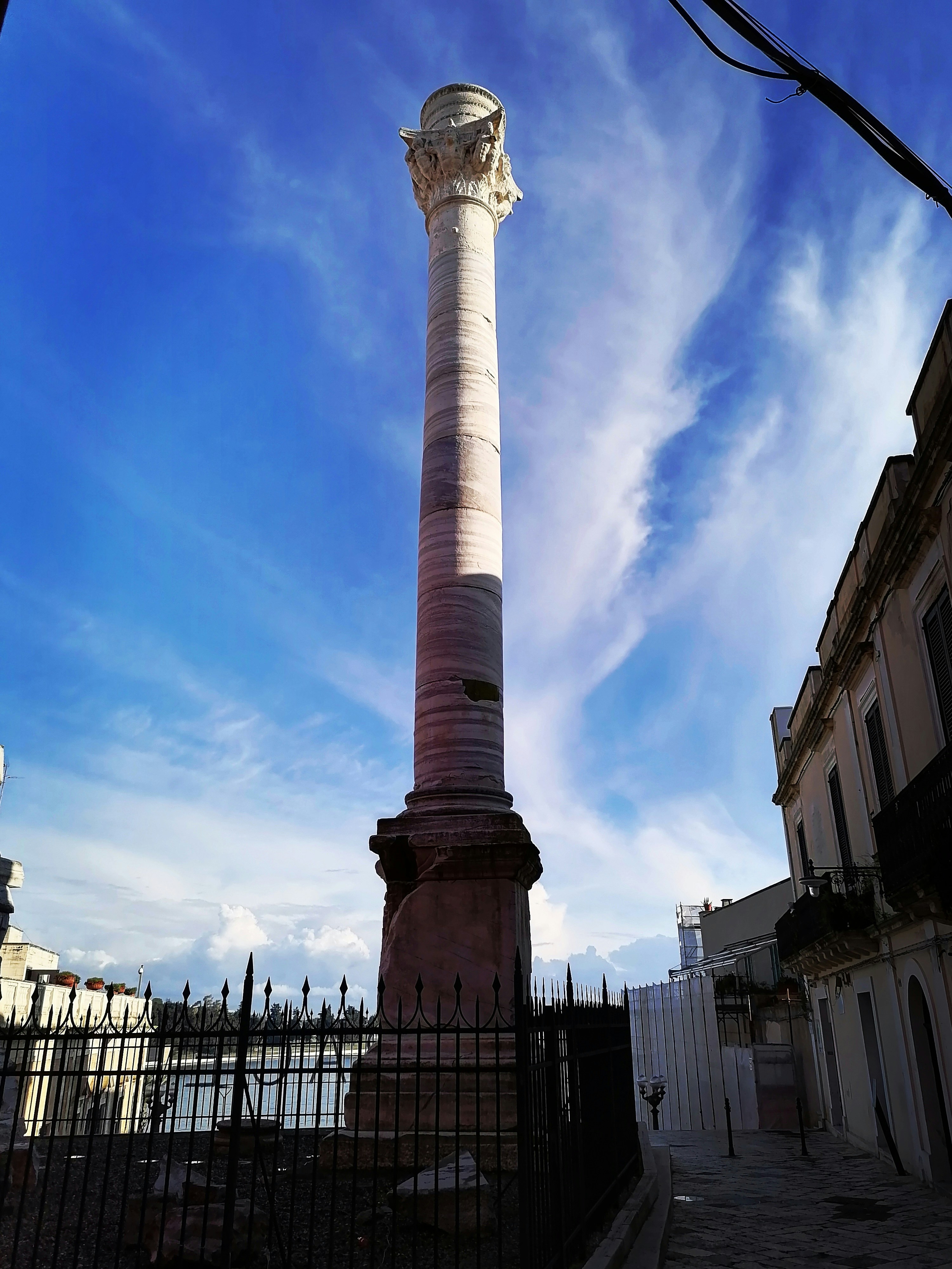 Tall white column towers over a quiet street against a vibrant blue sky.