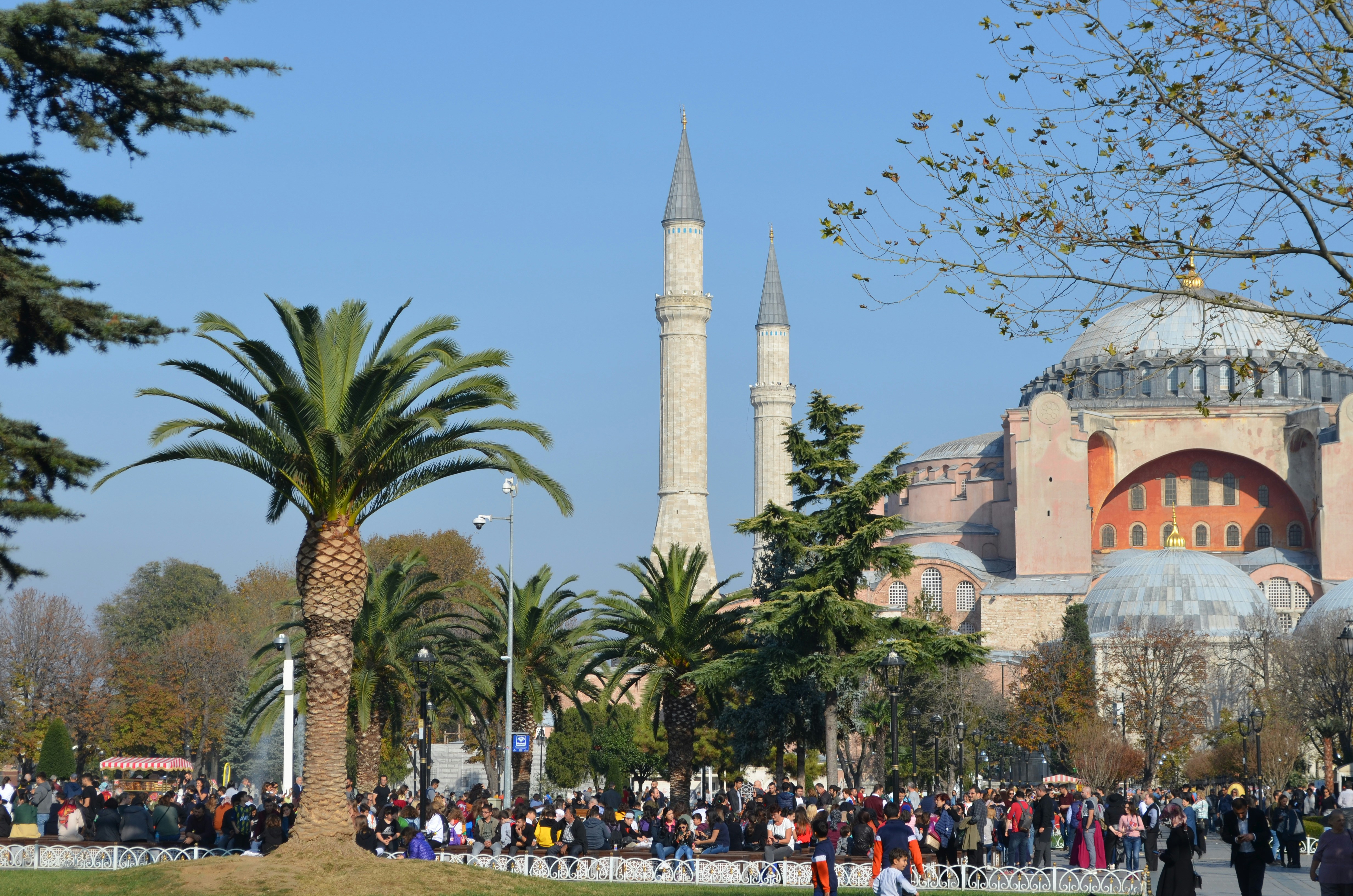 Crowd at the Front Courtyard of a Historic Mosque with Minarets and Palm Trees