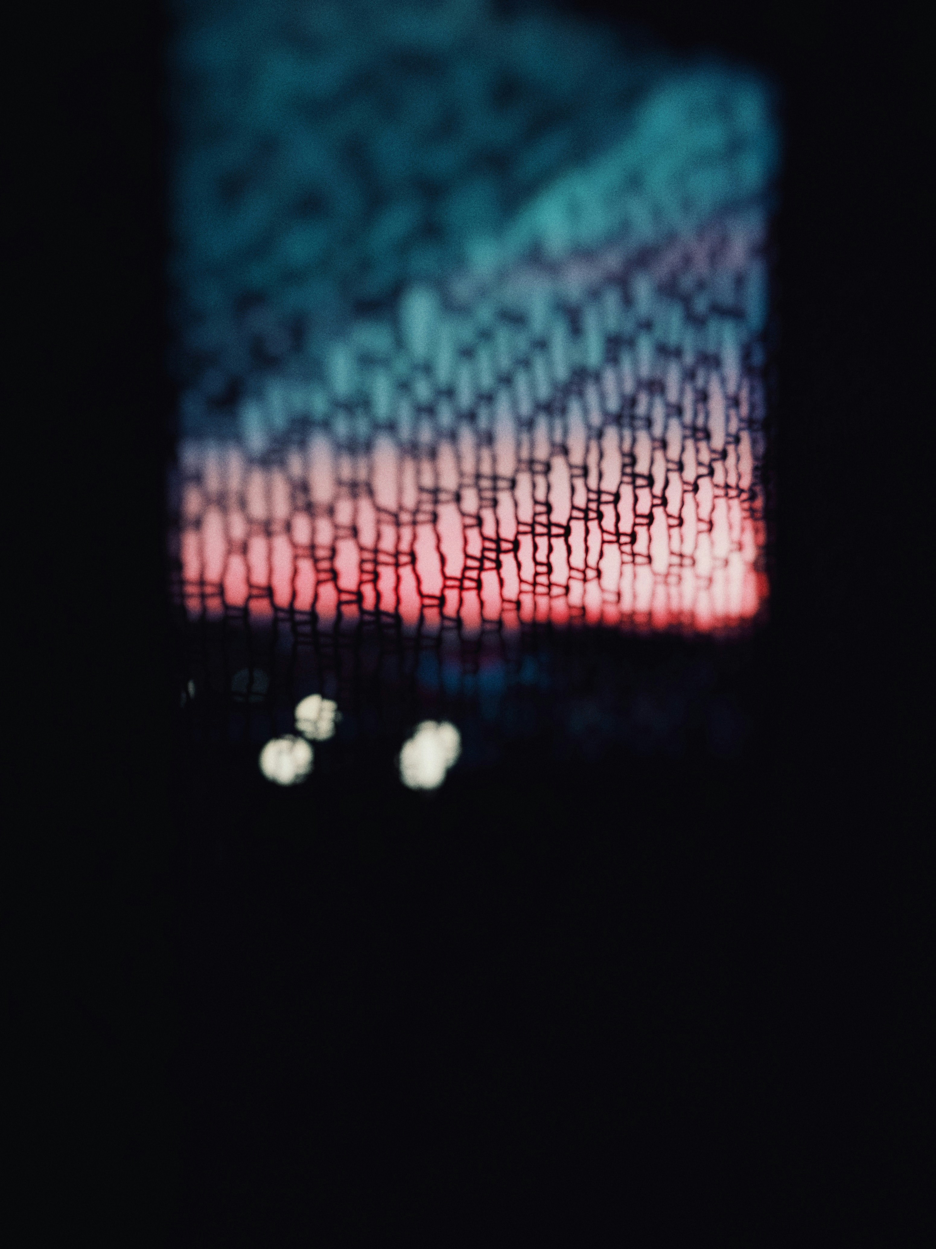 Intricate mesh pattern framing a vibrant twilight sky with hues of pink and blue. The scene captures the transition from day to night.