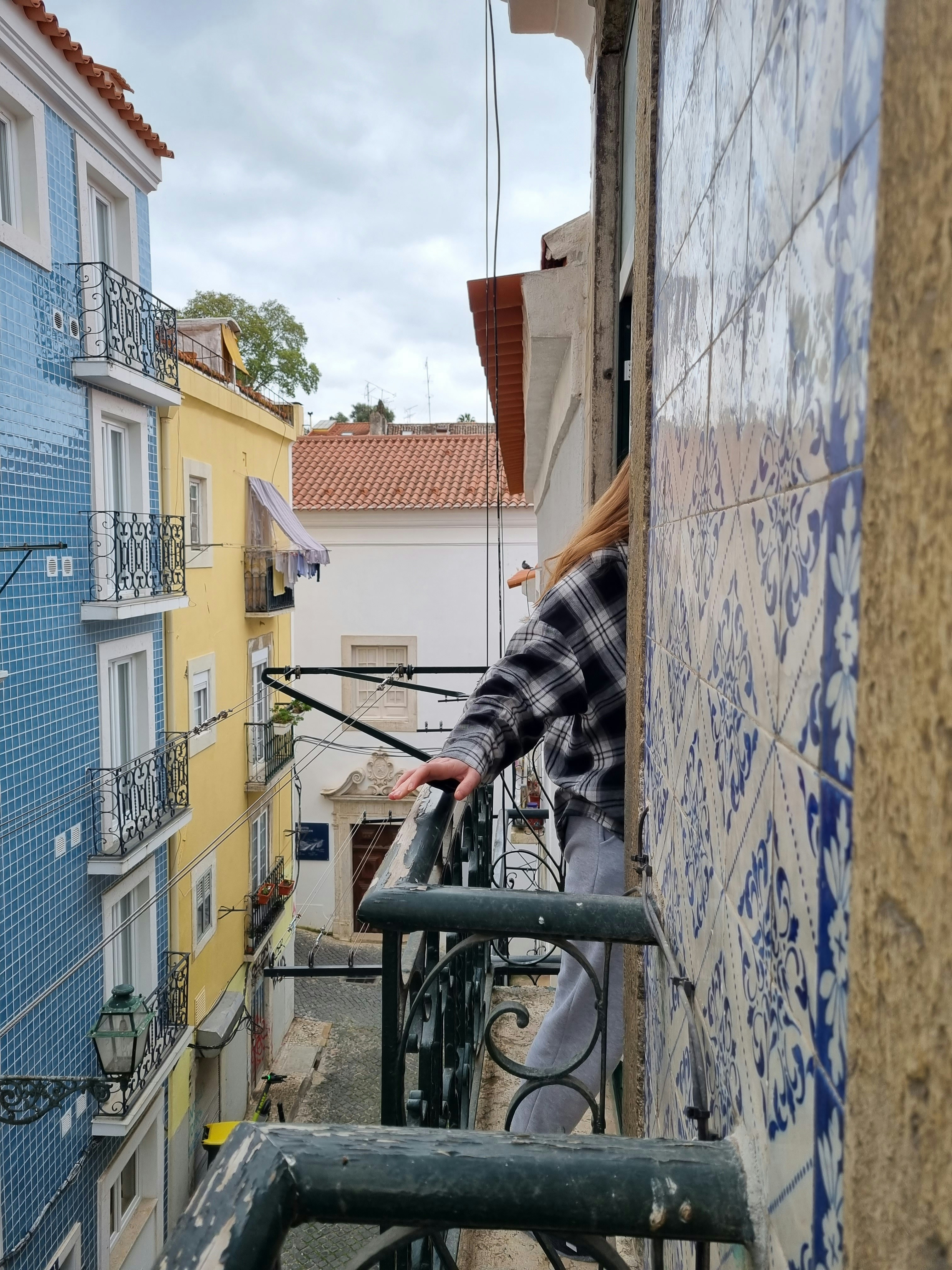 Between Tiles and Rails: A Hand Reaches Out Over a Colorful City Balcony