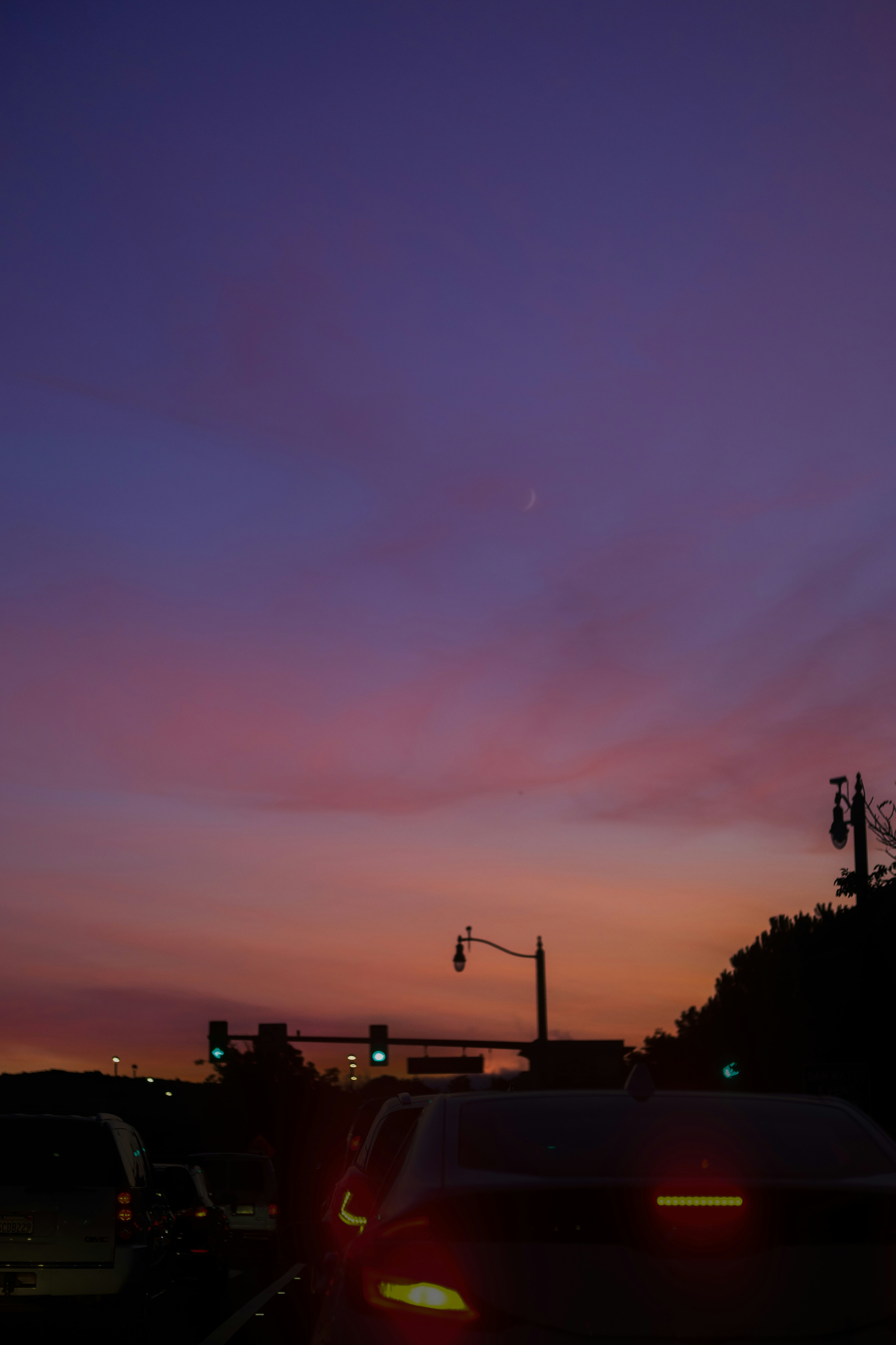 Cars stopped at a traffic light against a vibrant sunset sky with shades of purple and orange.