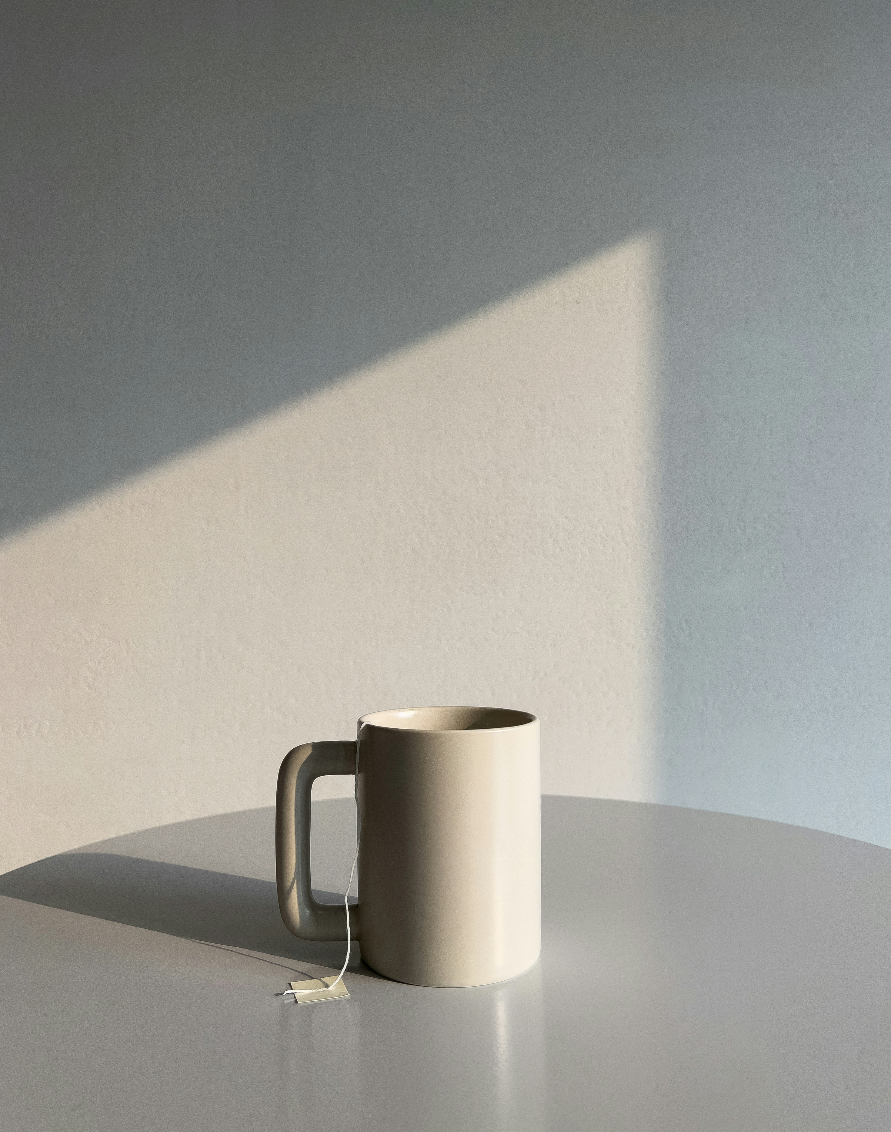 Minimalistic ceramic mug with a tea bag resting on a smooth table, illuminated by soft natural light.