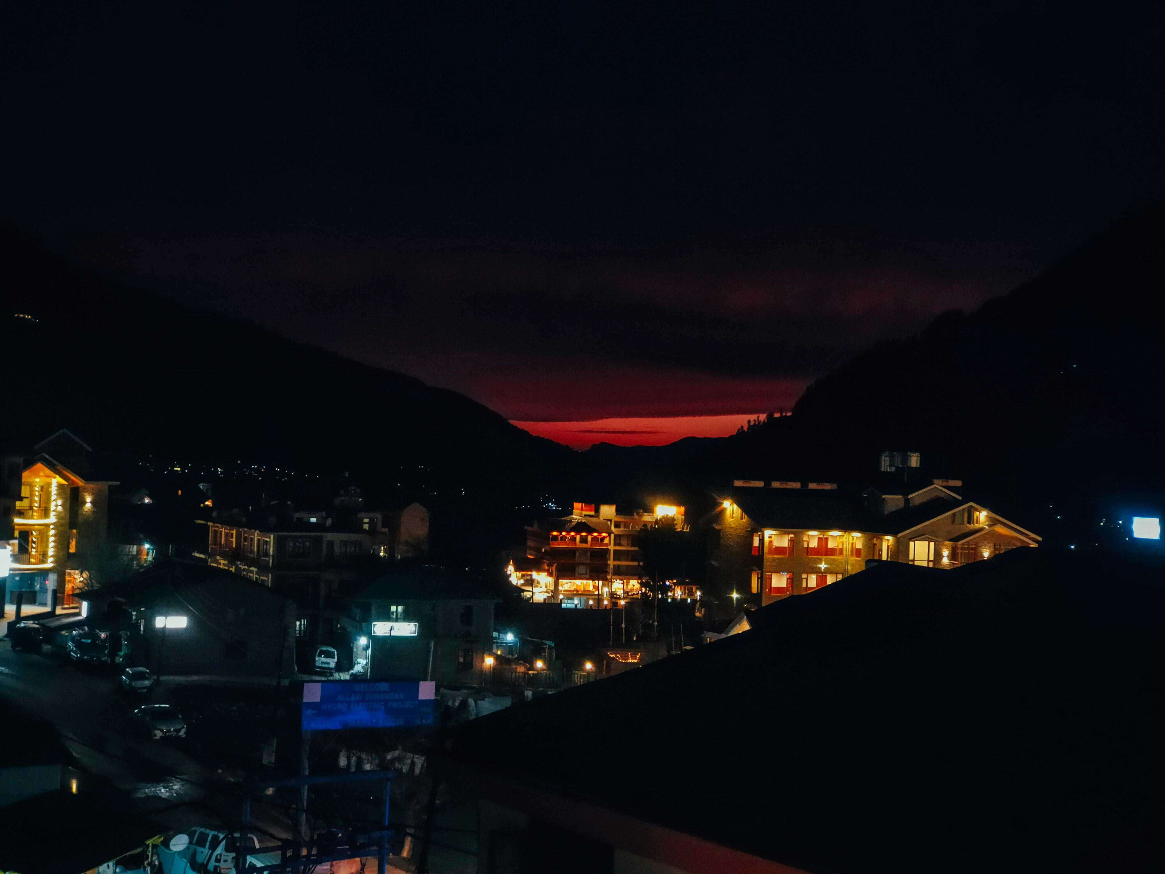 A serene twilight scene showcasing a mountain town illuminated by warm lights against a darkening sky. The horizon glows with a hint of sunset.