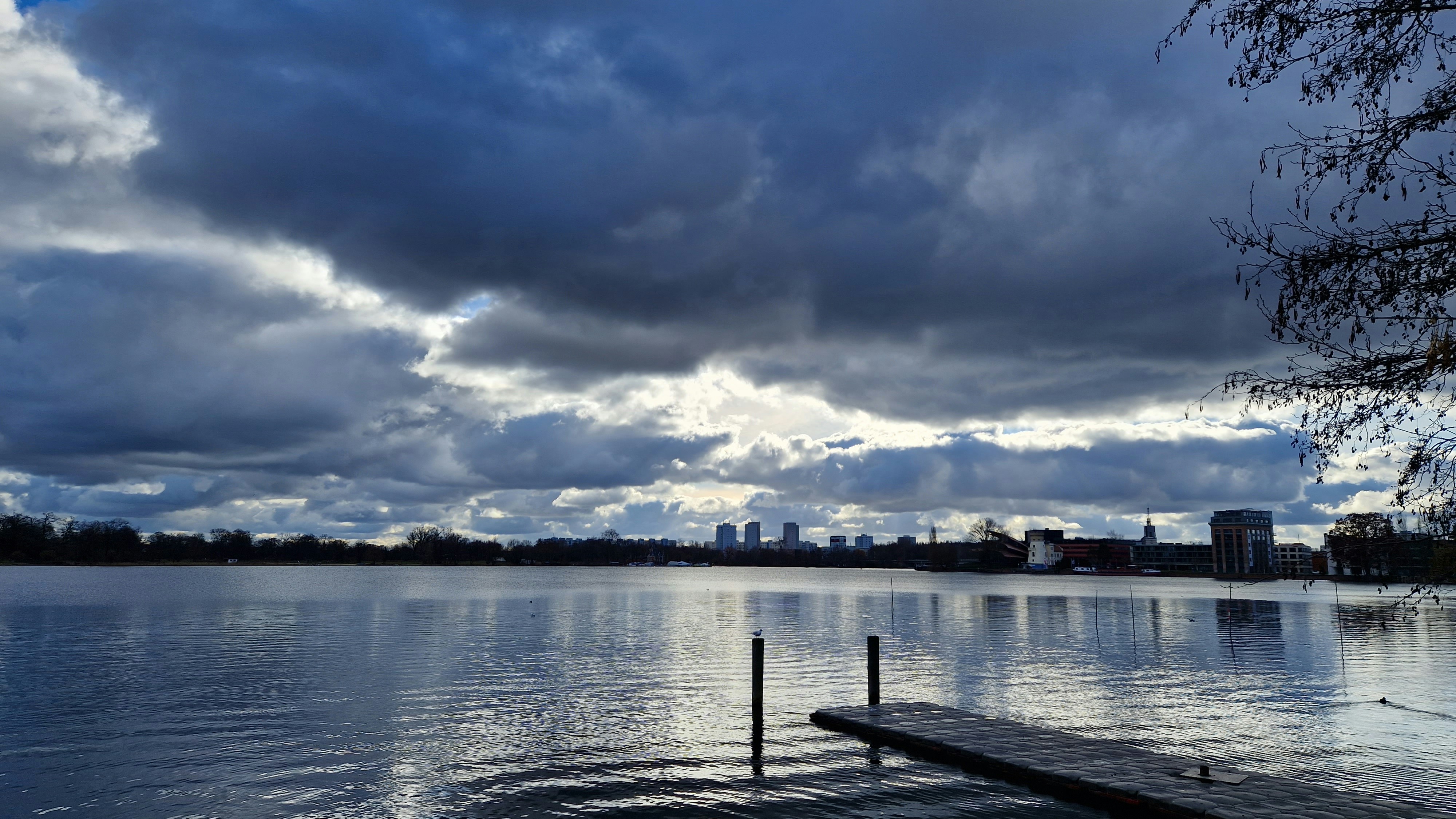 Cloud-laden sky reflects on a calm lake with a silhouetted pier extending into the water.