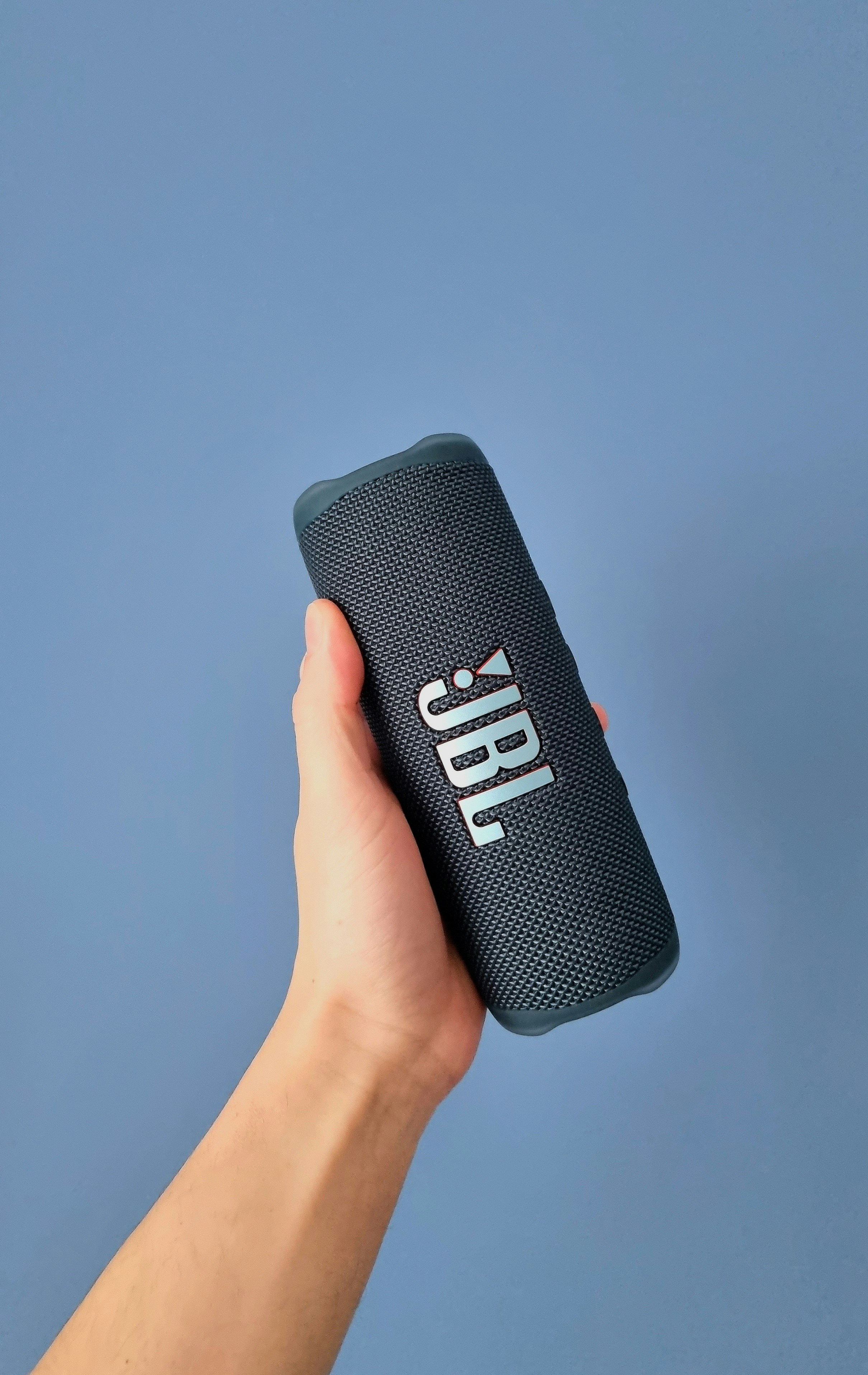 Grip and Groove: A JBL Speaker Clutched Against a Soft Blue Backdrop