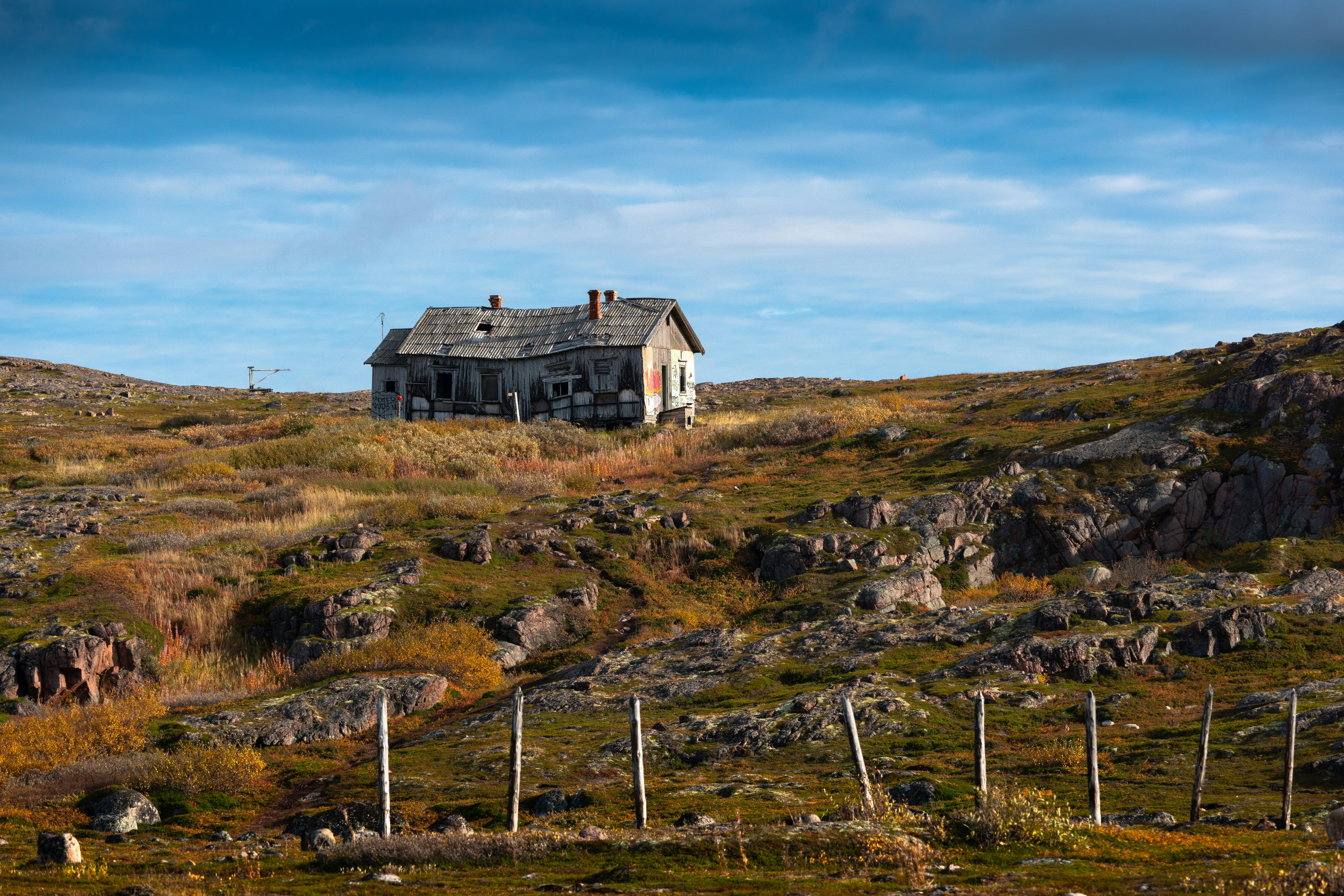 Rustic house perched on a rocky hill under a vibrant blue sky.