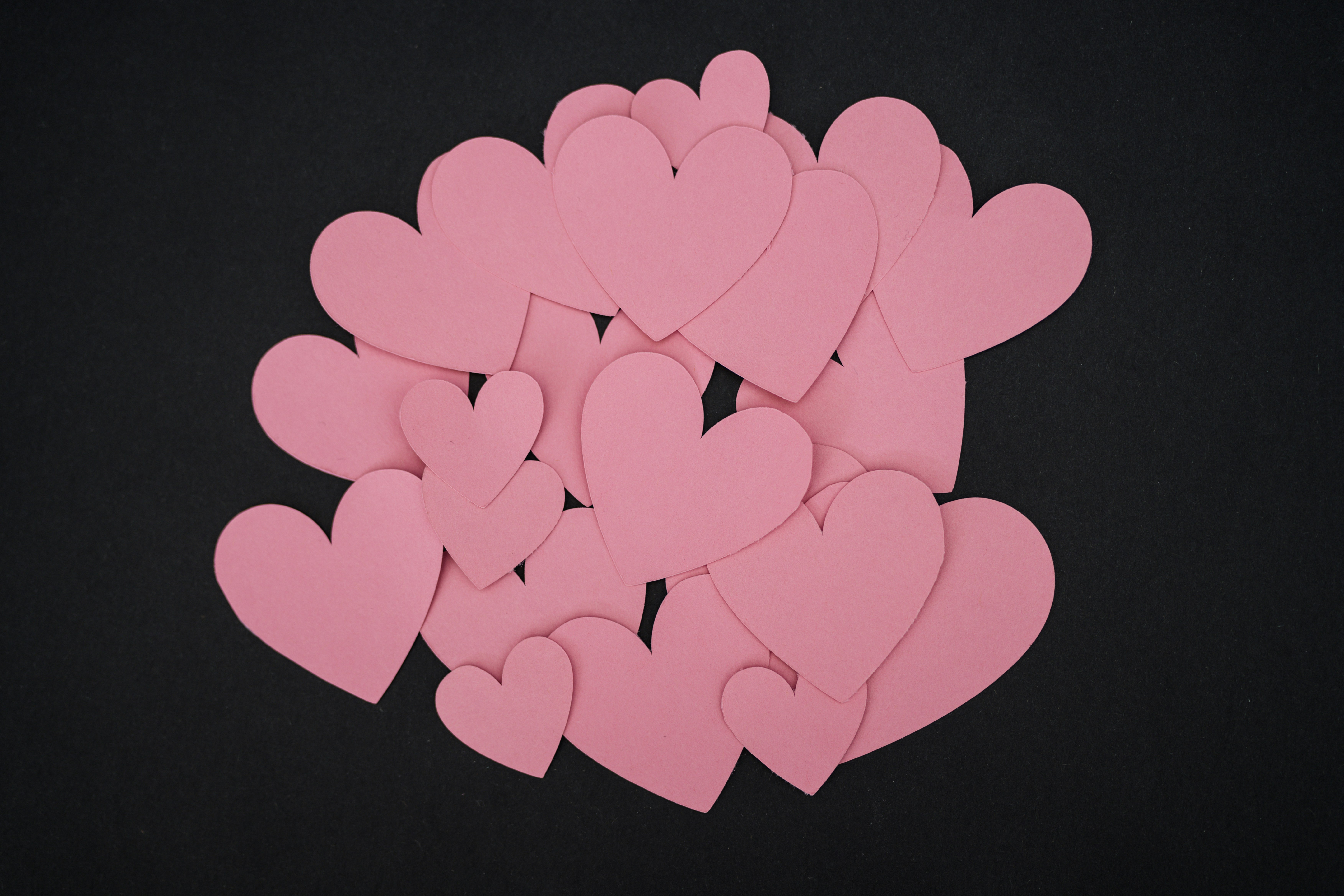 A pile of pink paper hearts on a black background photo – Free Love ...