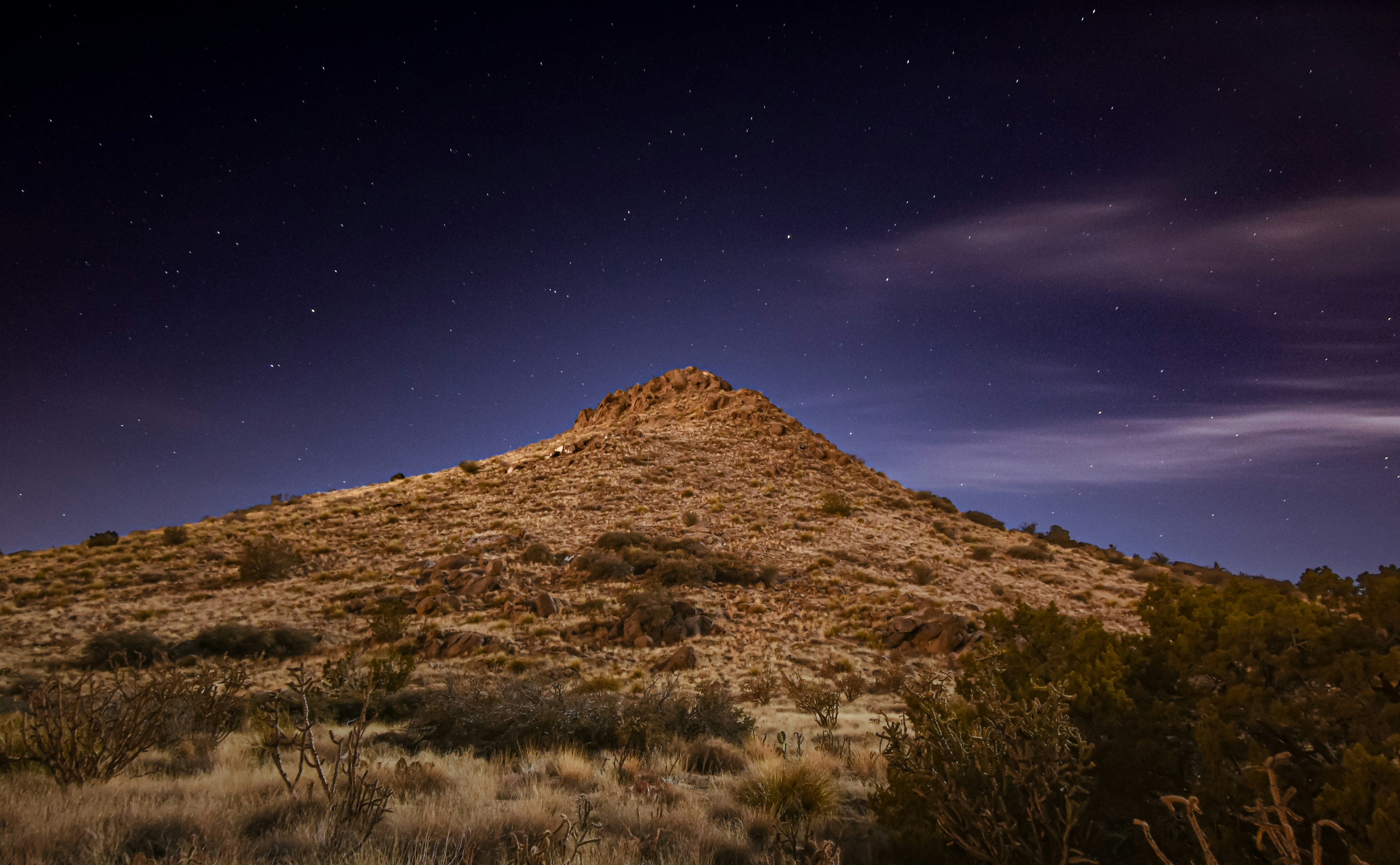 Desert mountain under a starry night sky with faint clouds.