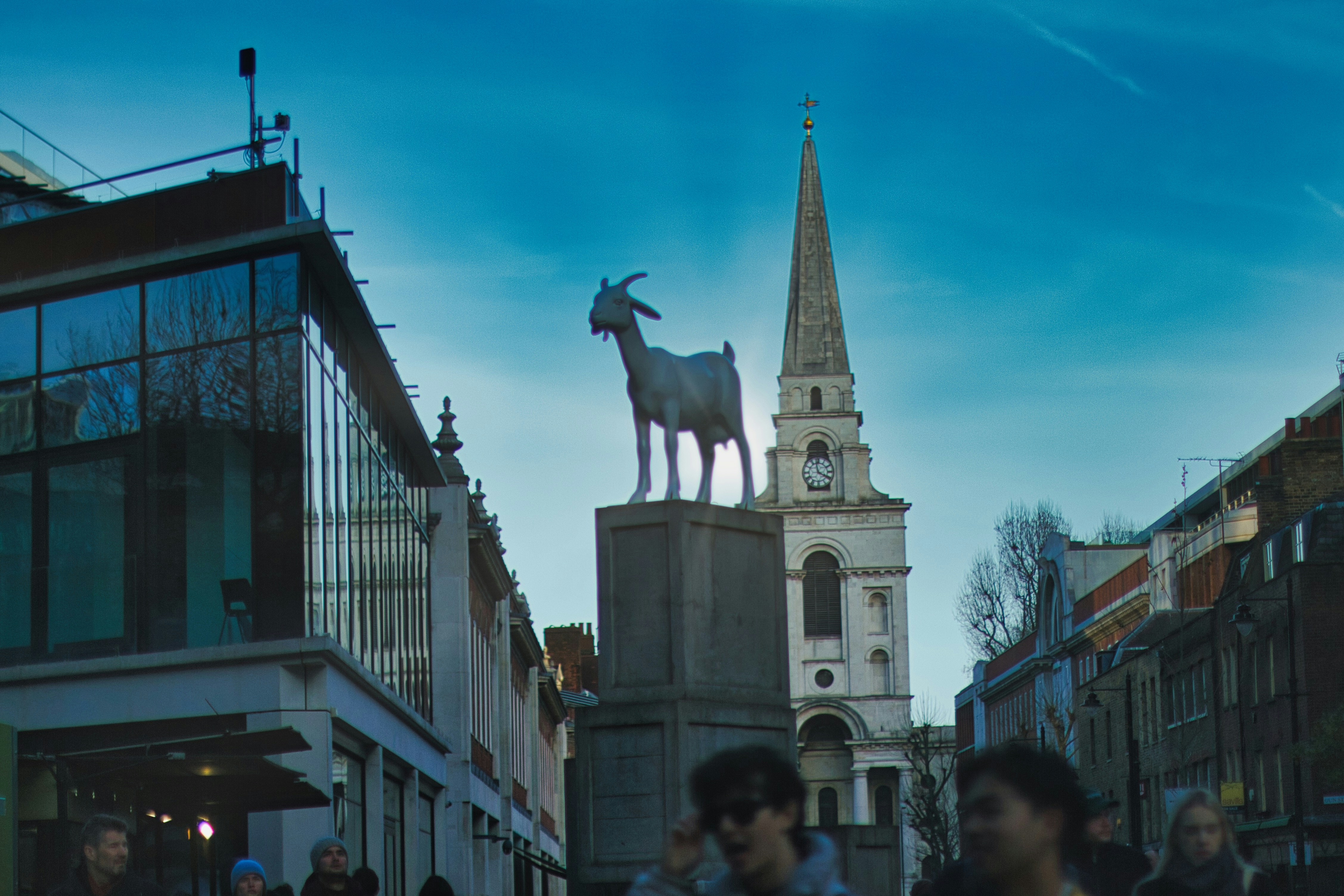 Goat Statue Overlooking a Sunlit Town Square with a Spired Church