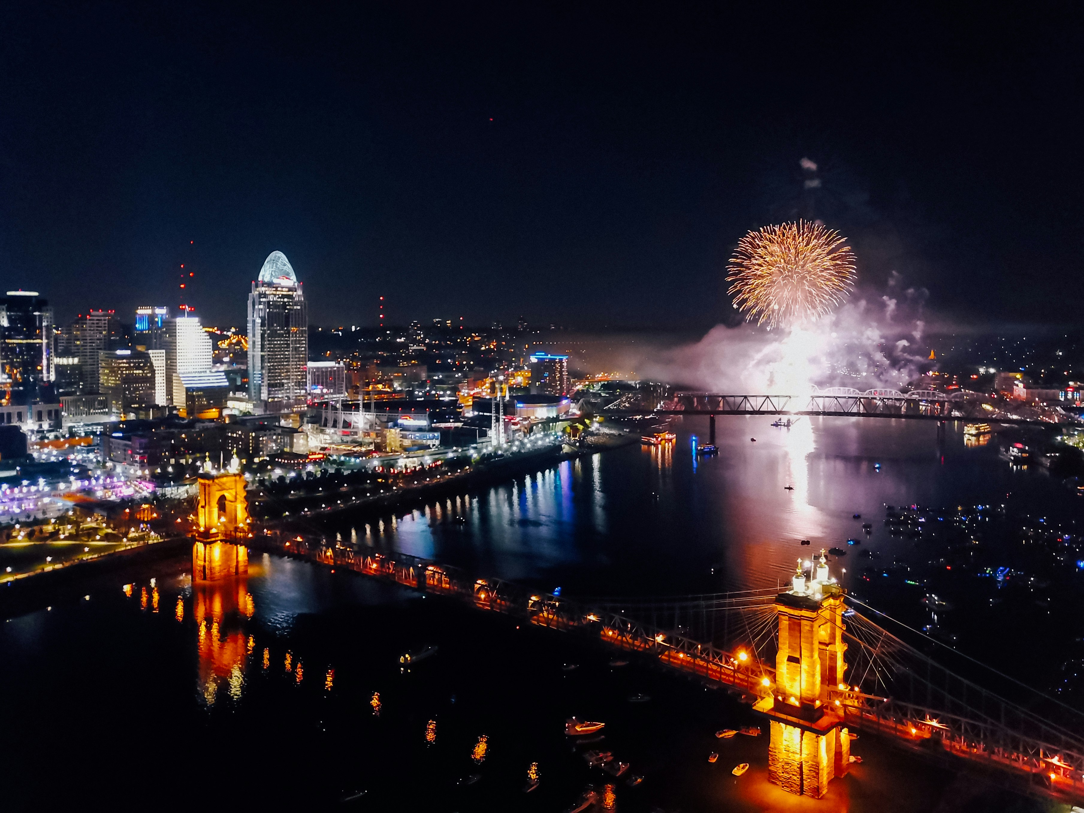Fireworks erupt over a vibrant city skyline reflecting in the river, showcasing the dynamic energy of a night celebration.
