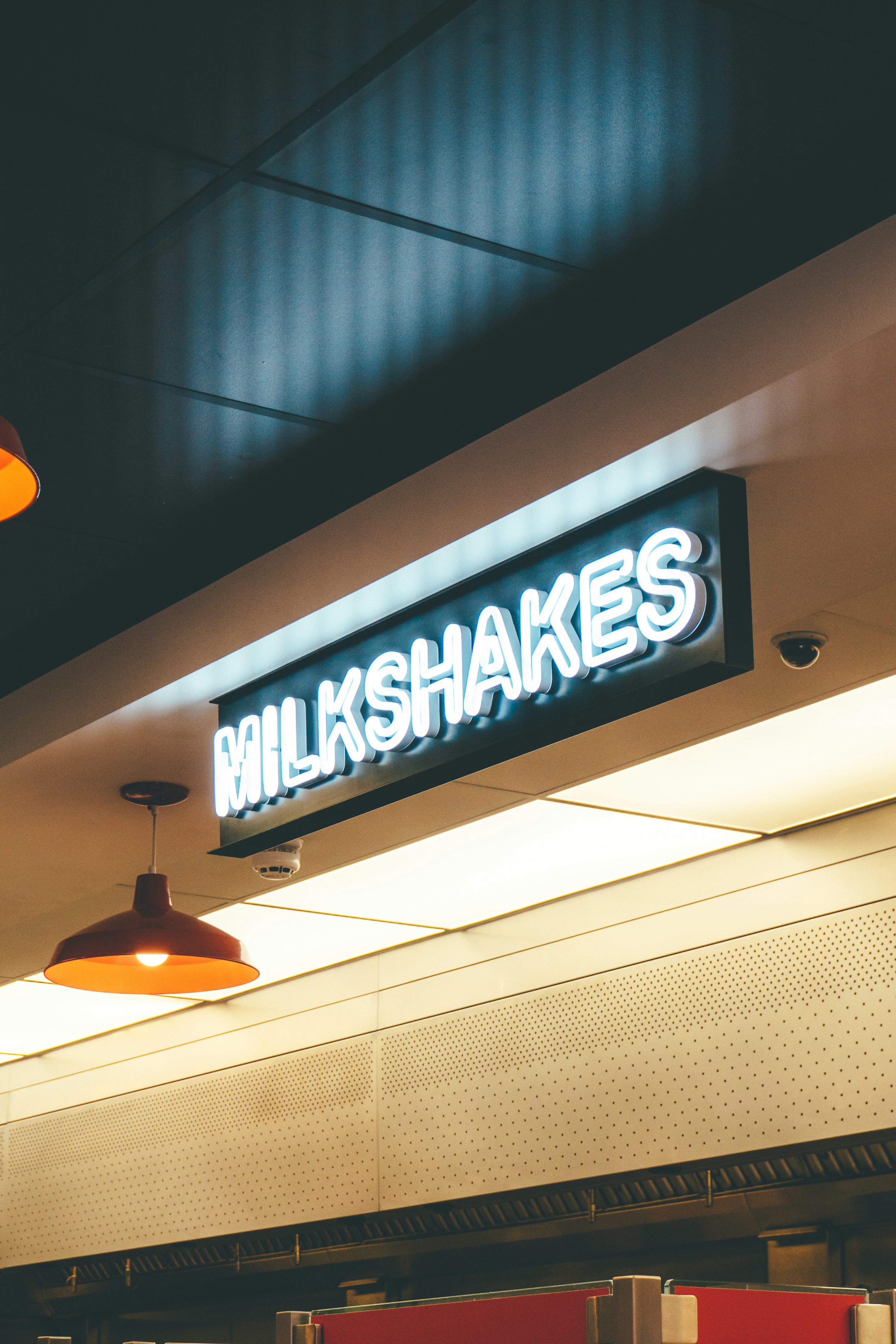 Neon sign displaying 'MILKSHAKES' with a warm ceiling light in a diner setting.