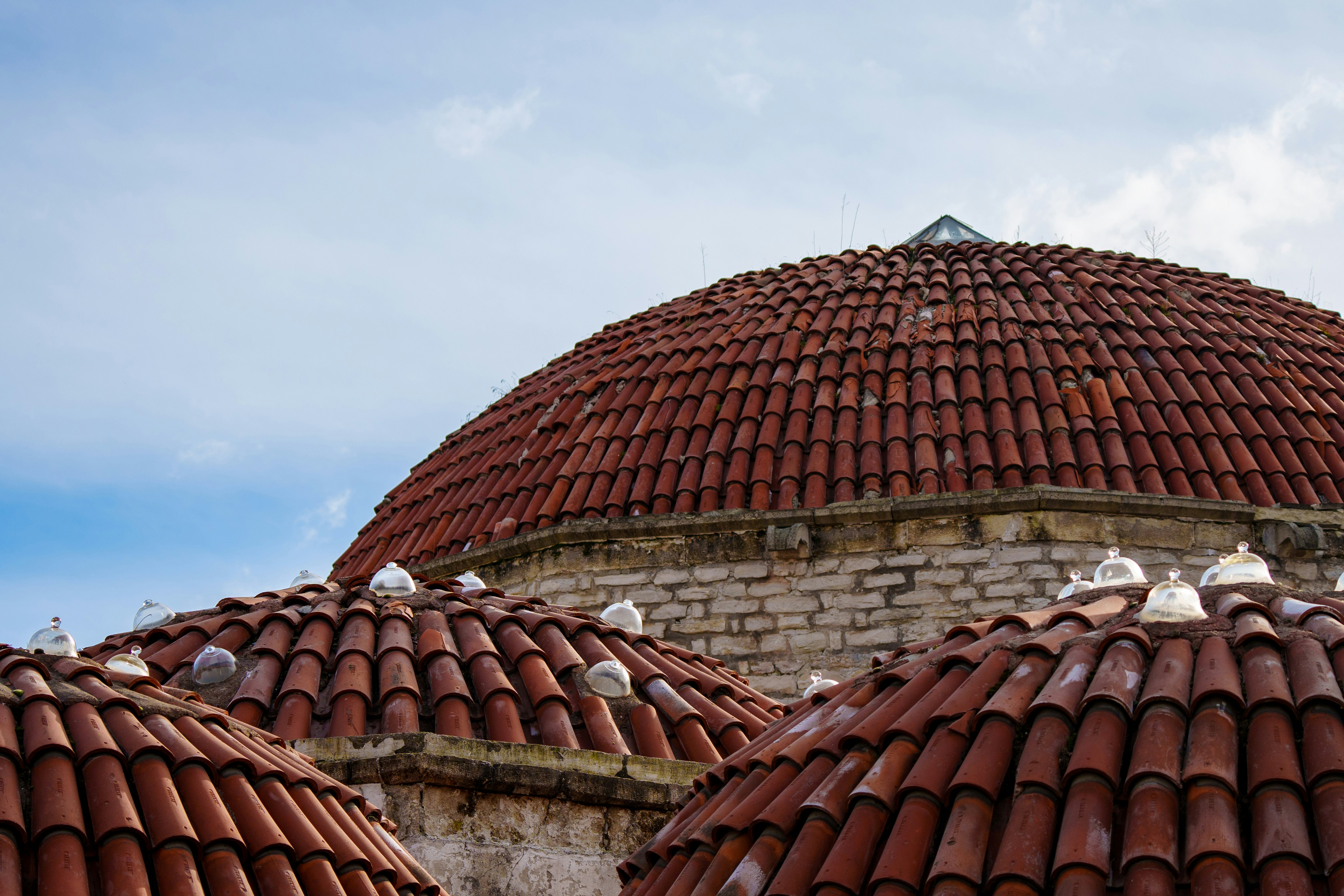 Red-tiled domes of a traditional building with intricate patterns under a partly cloudy sky.