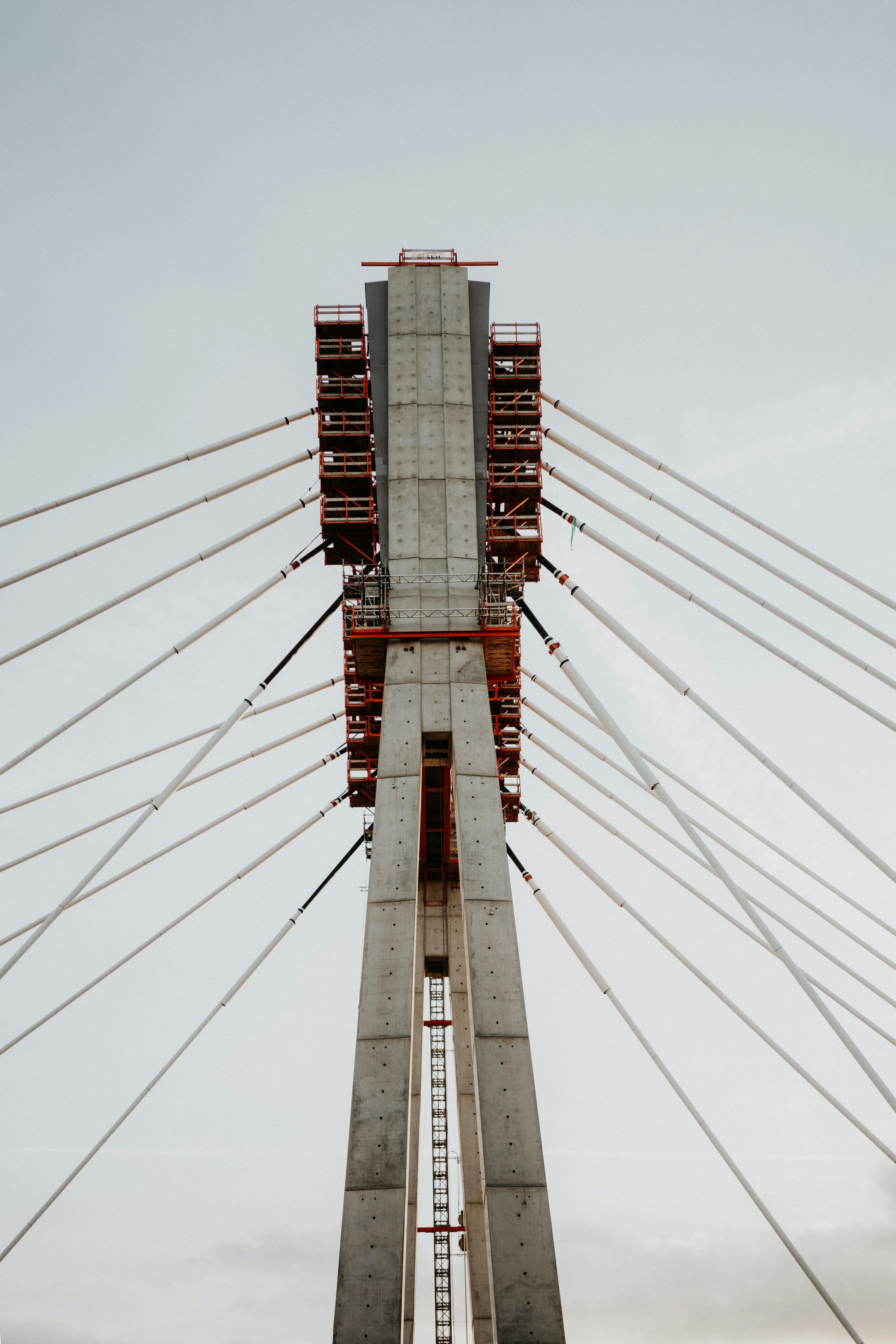 A towering concrete pylon supports a web of cables, showcasing the intricate design of modern engineering. The structure stands against a soft sky, emphasizing its monumental scale.