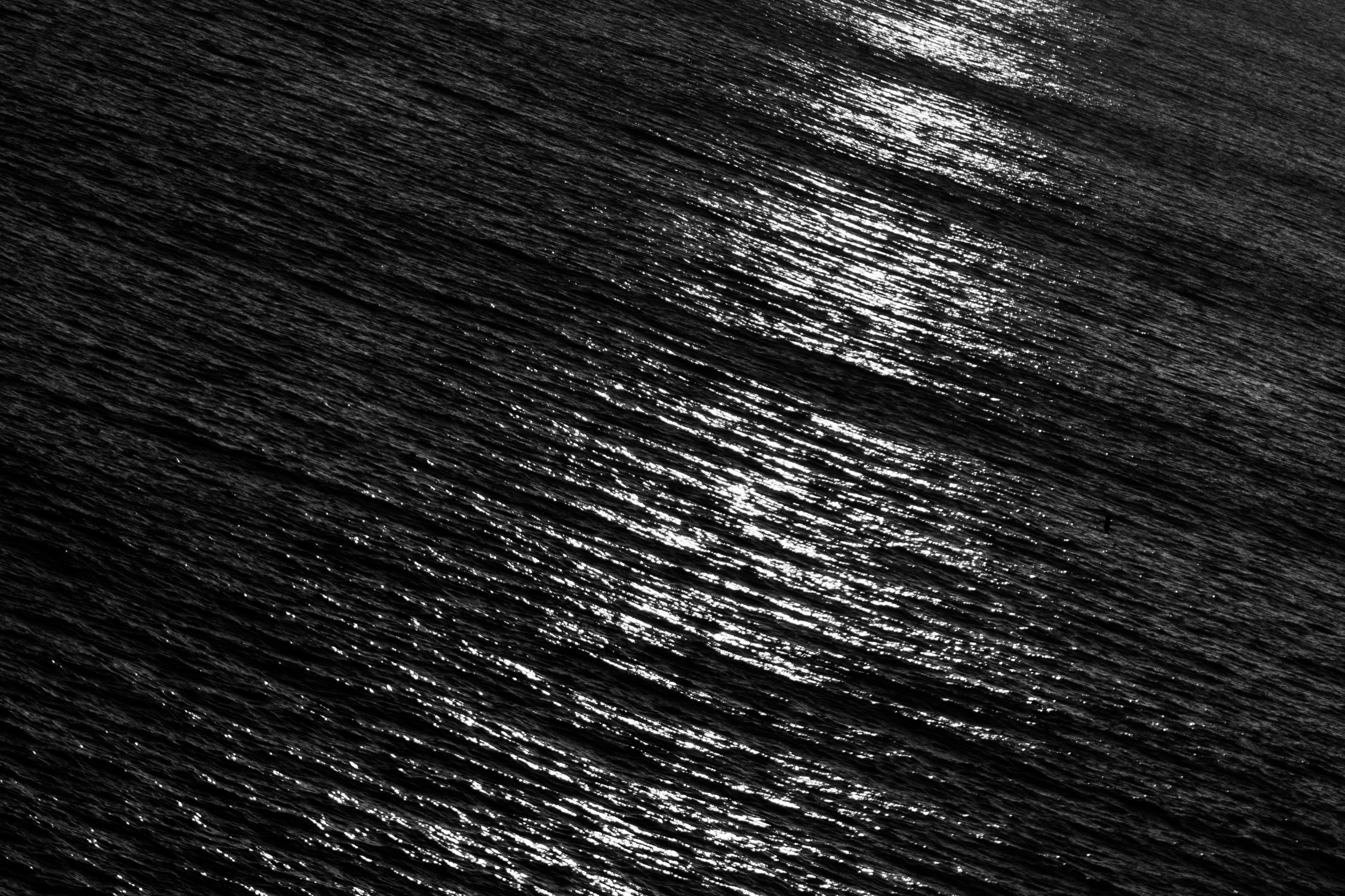 Glistening waves reflect light in a mesmerizing pattern, creating an abstract interplay of shadows and highlights on the surface.