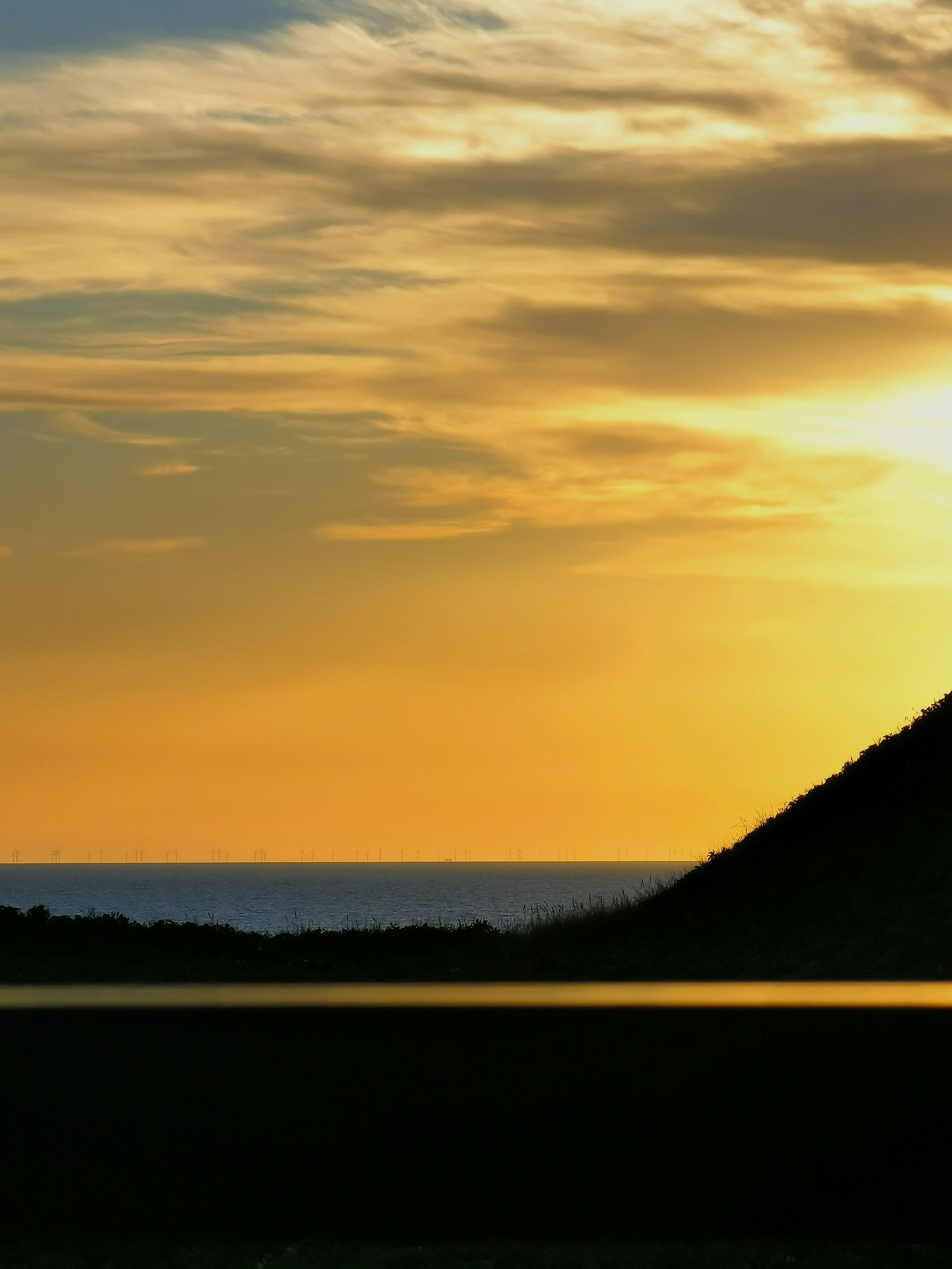 Sunset silhouette over a grassy ridge by the sea