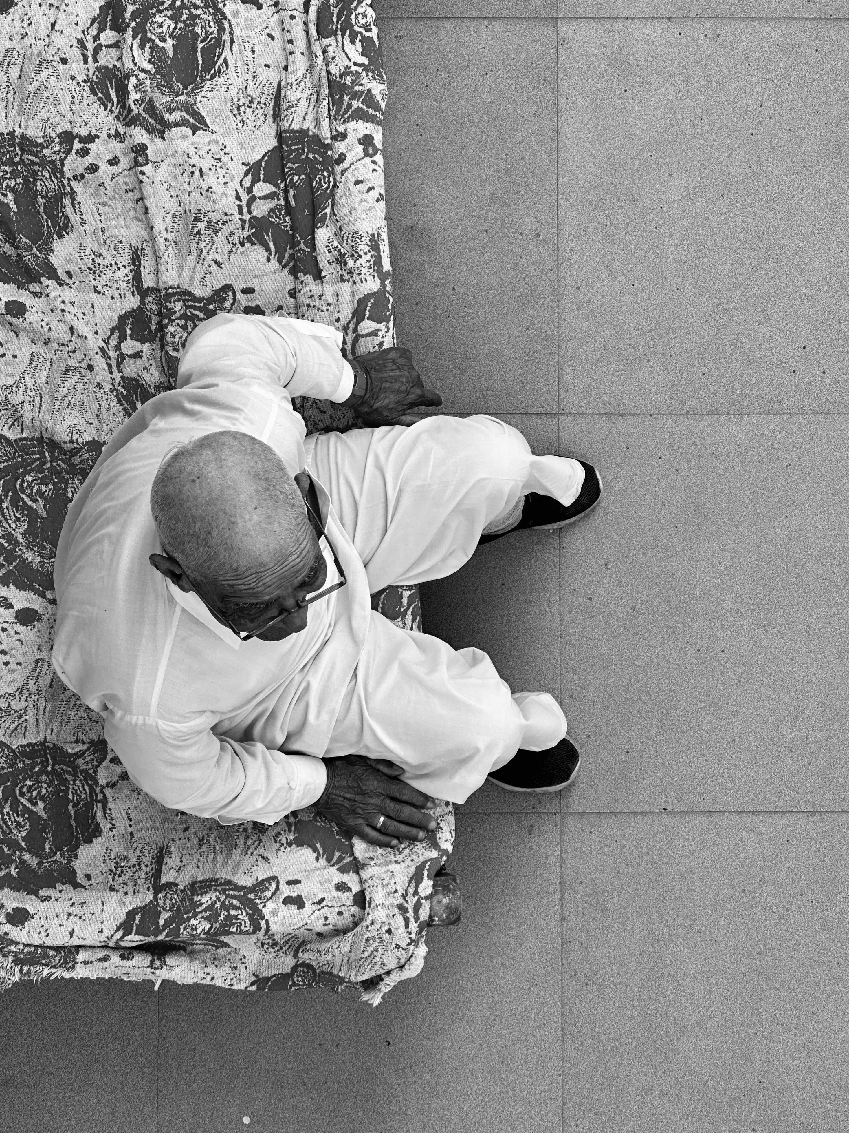 Bird’s-eye Quiet: White-clad figure framed on a floral sofa from above