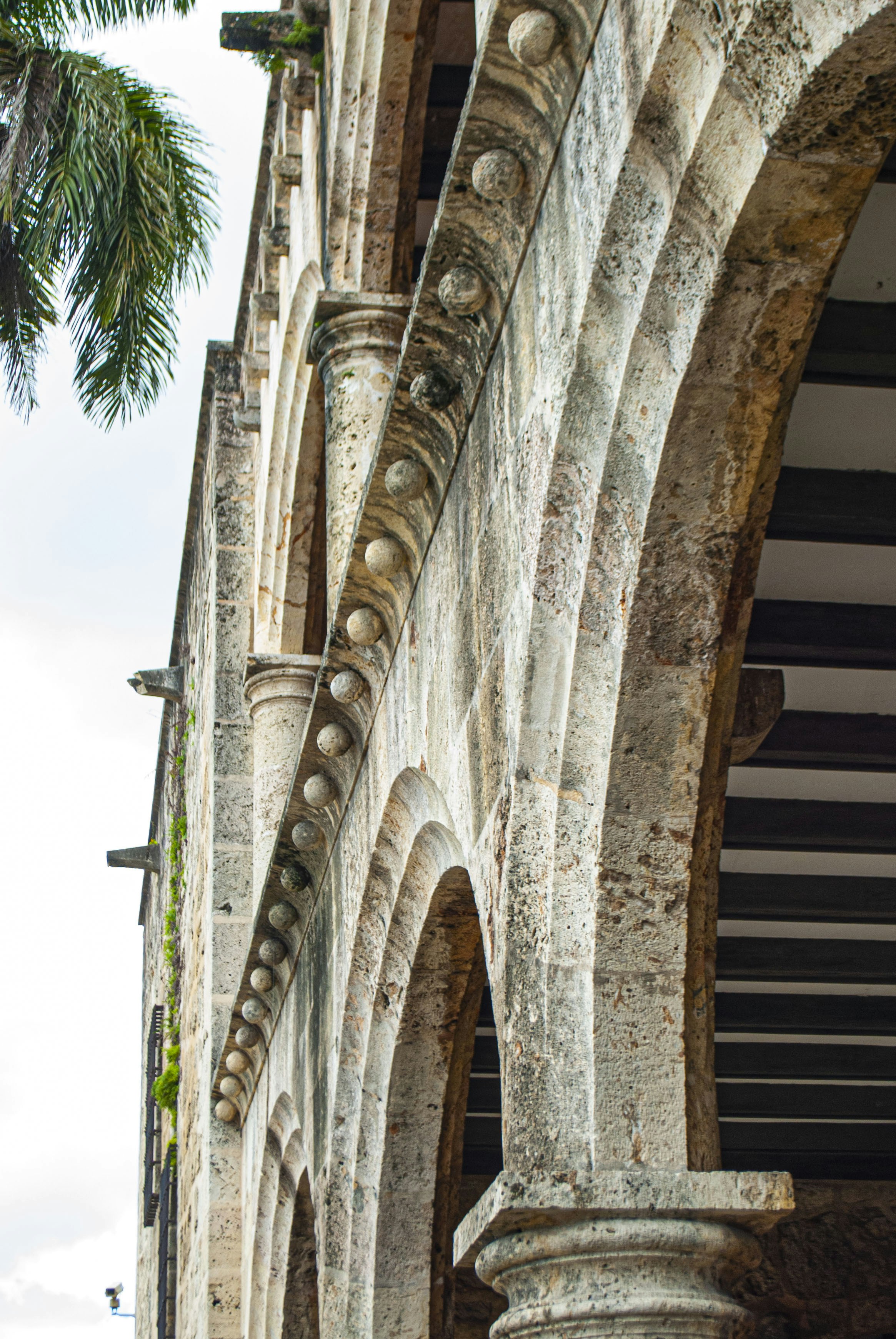 Intricate stone arches adorned with decorative elements, framed by lush greenery and a hint of sky above.