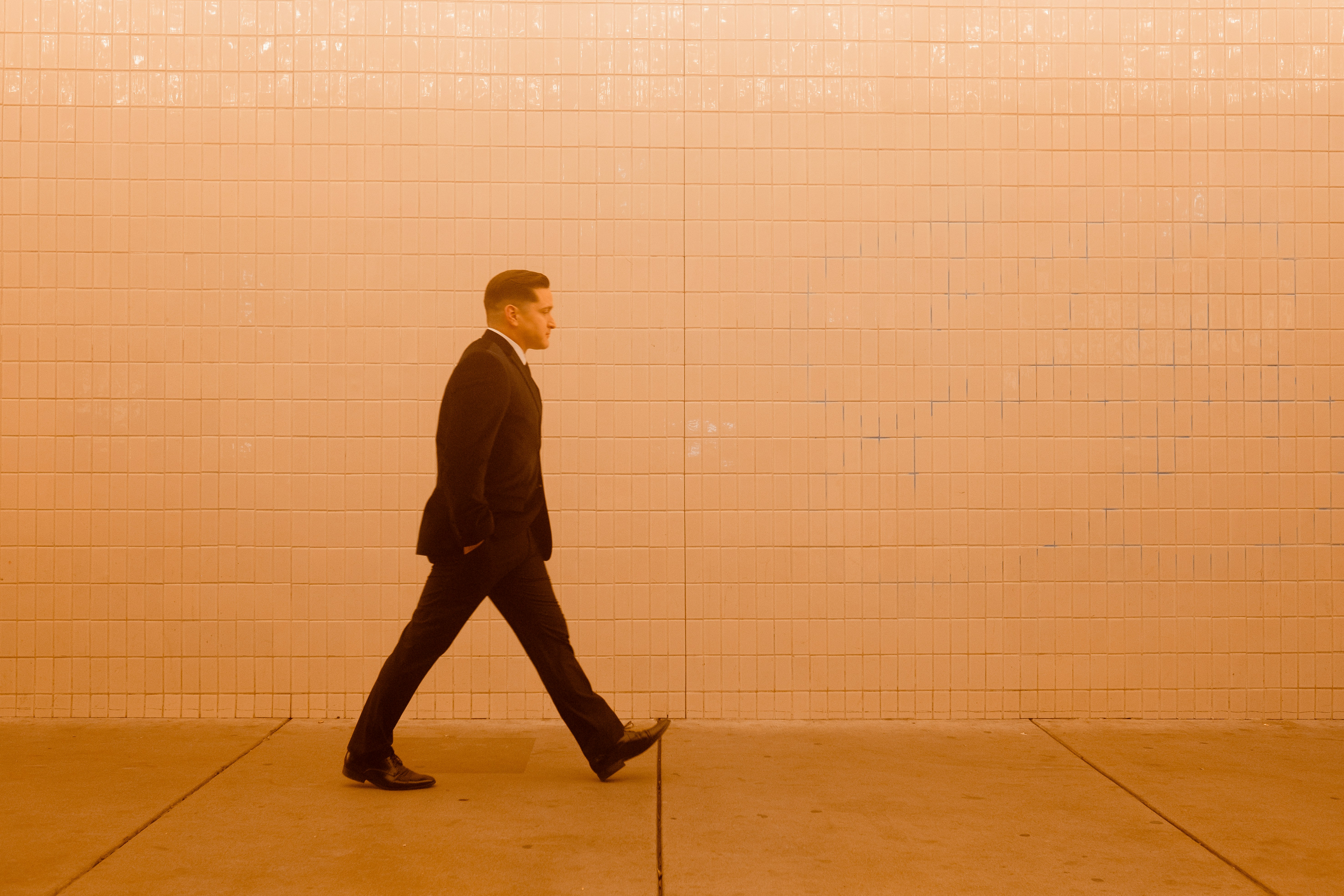 Lone Executive Steps Across an Amber-Tiled Corridor