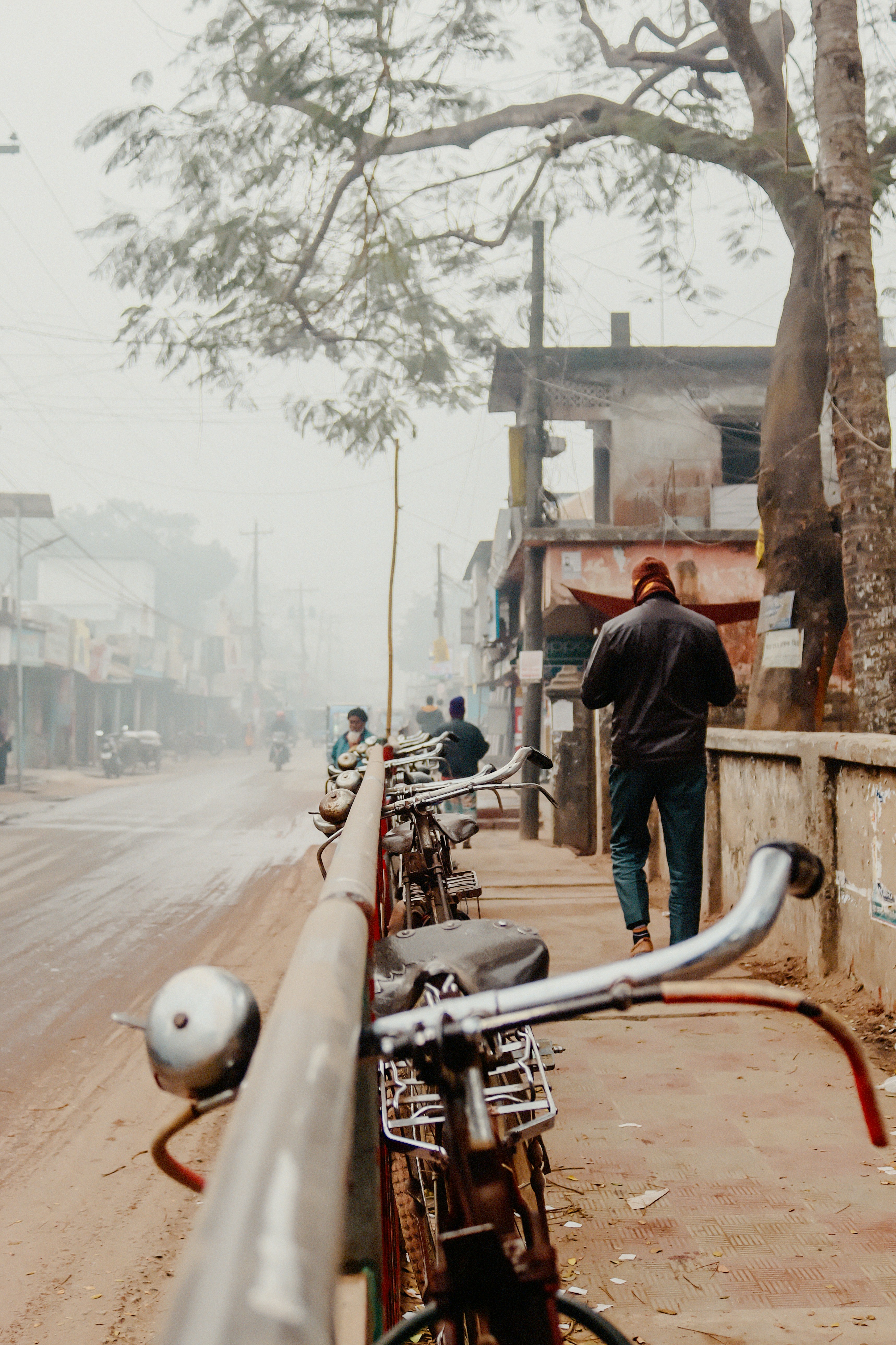 Fogbound Boulevard: A lone figure beside bicycles on a misty, dawn-lit street