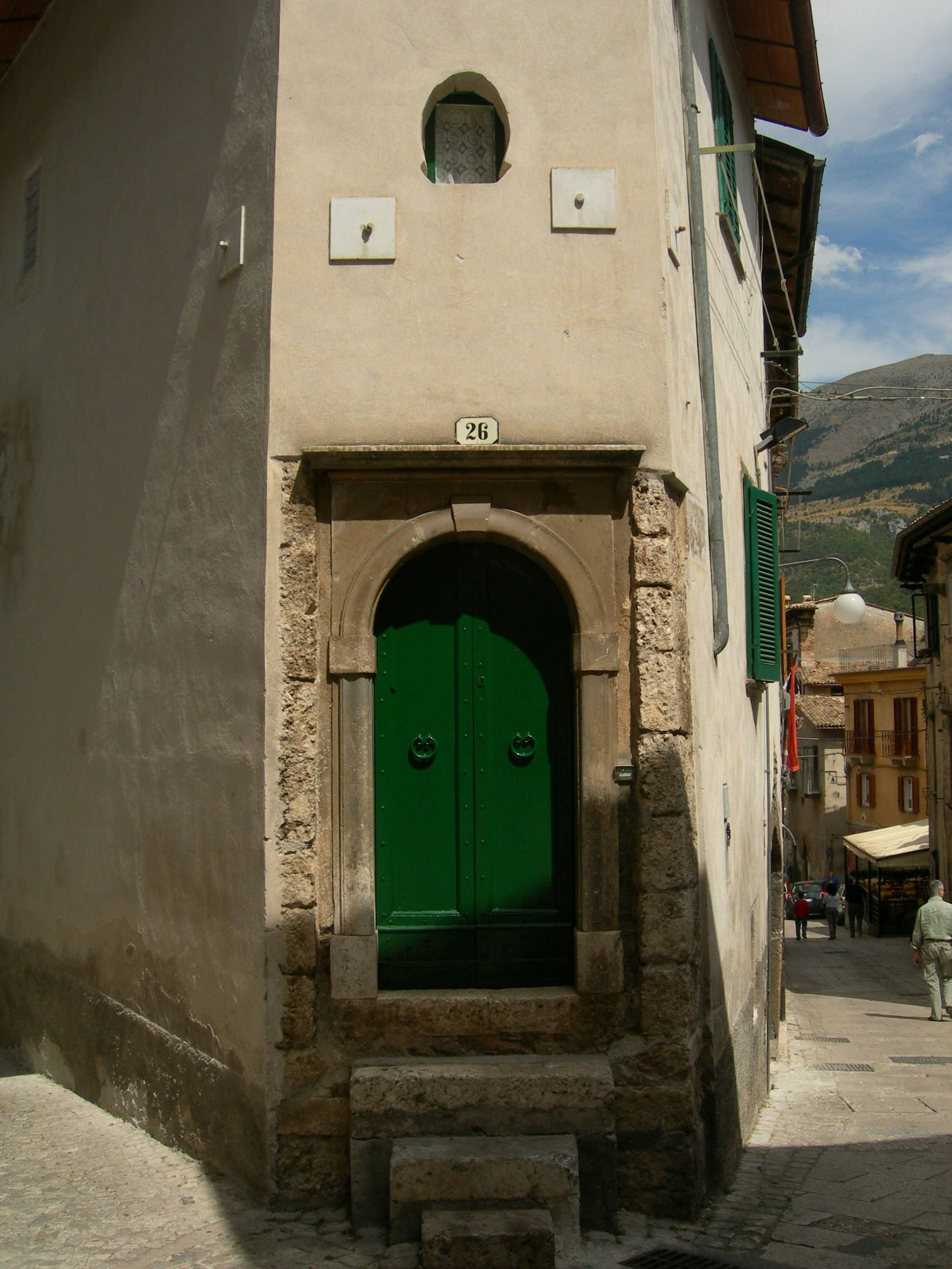 Photograph of a narrow alpine street with a bold green arched door set in a weathered stone facade.