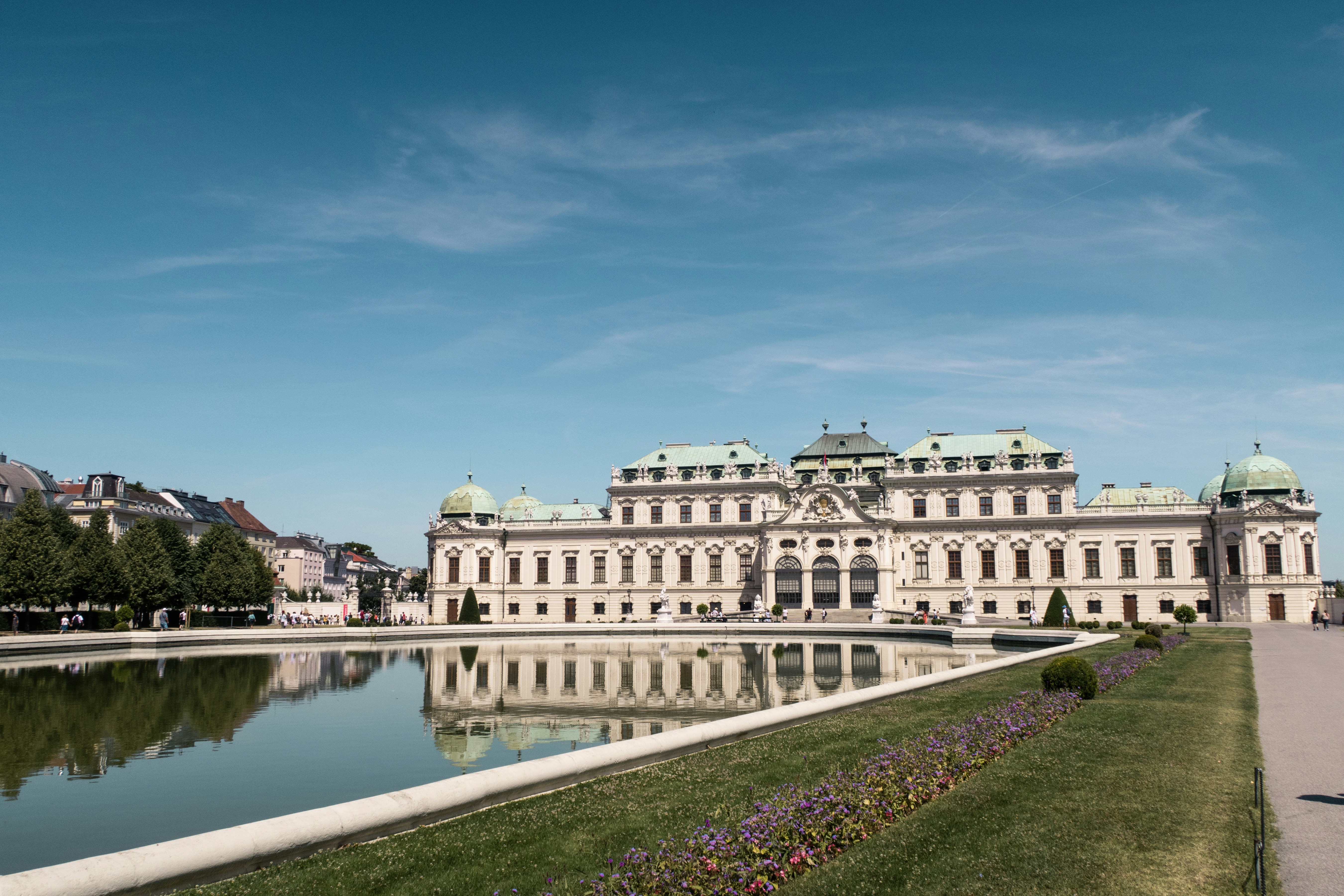 Belvedere Palace reflected in a serene pond, surrounded by manicured gardens under a clear blue sky.