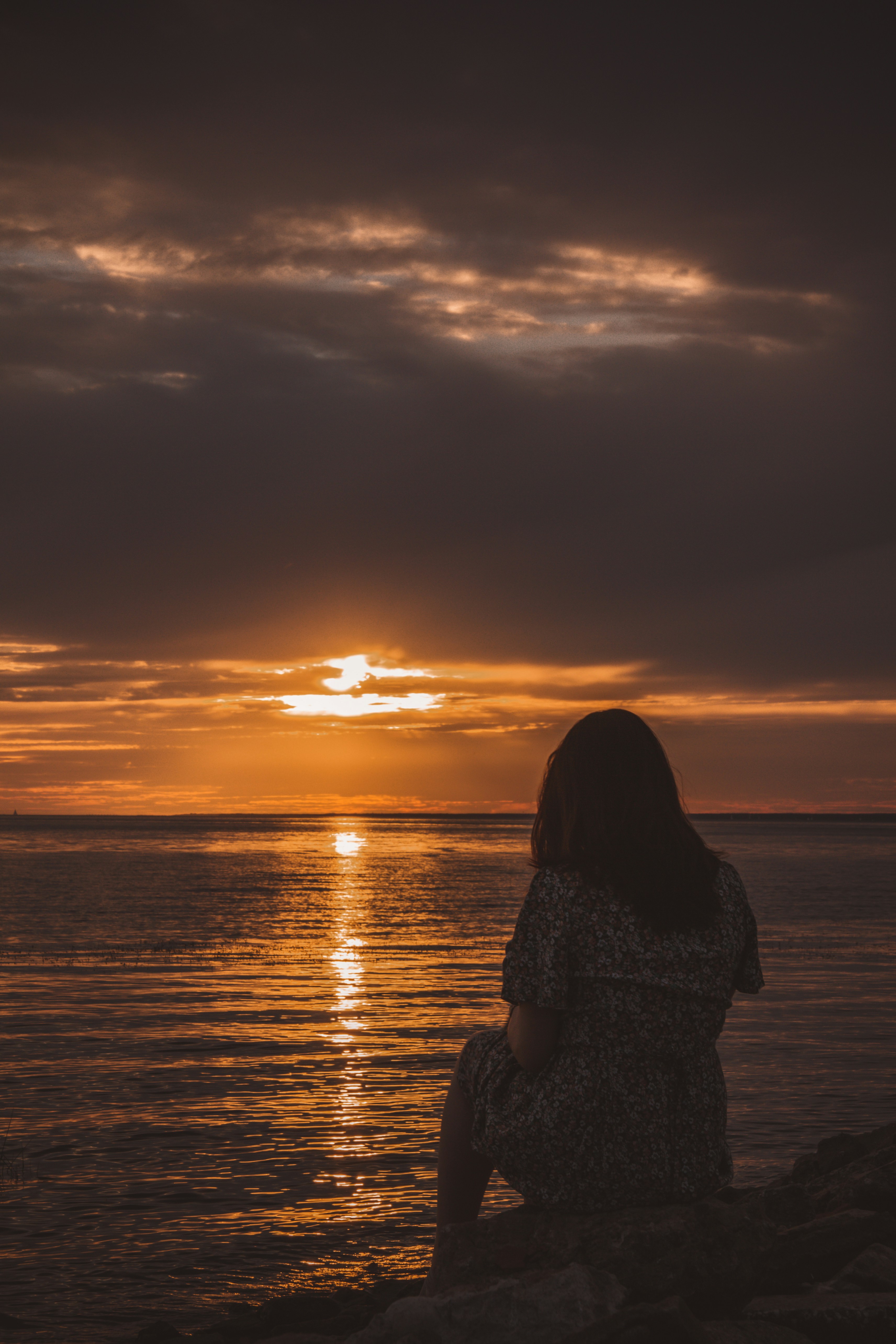 A woman sitting on a rock watching the sunset photo – Free Nature Image ...