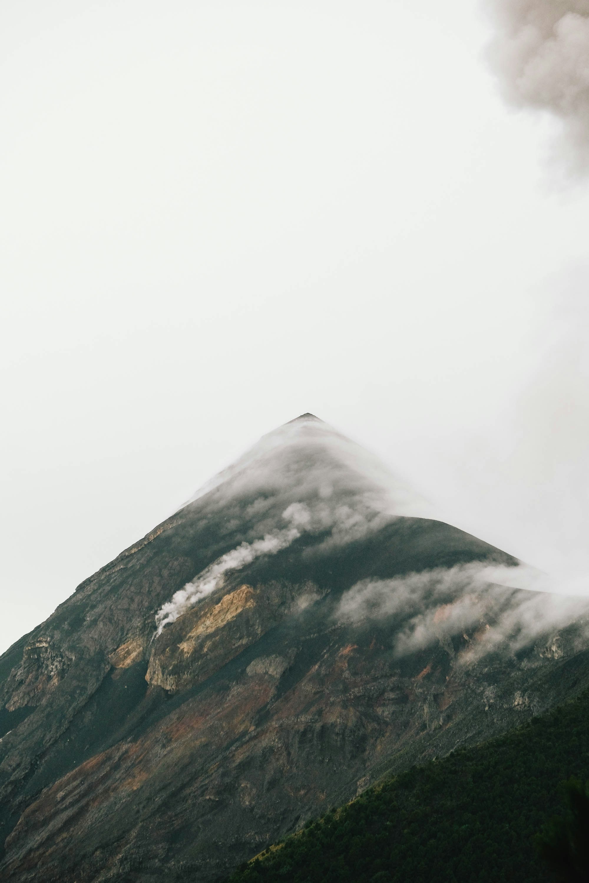 Volcano | a very tall mountain covered in clouds and smoke