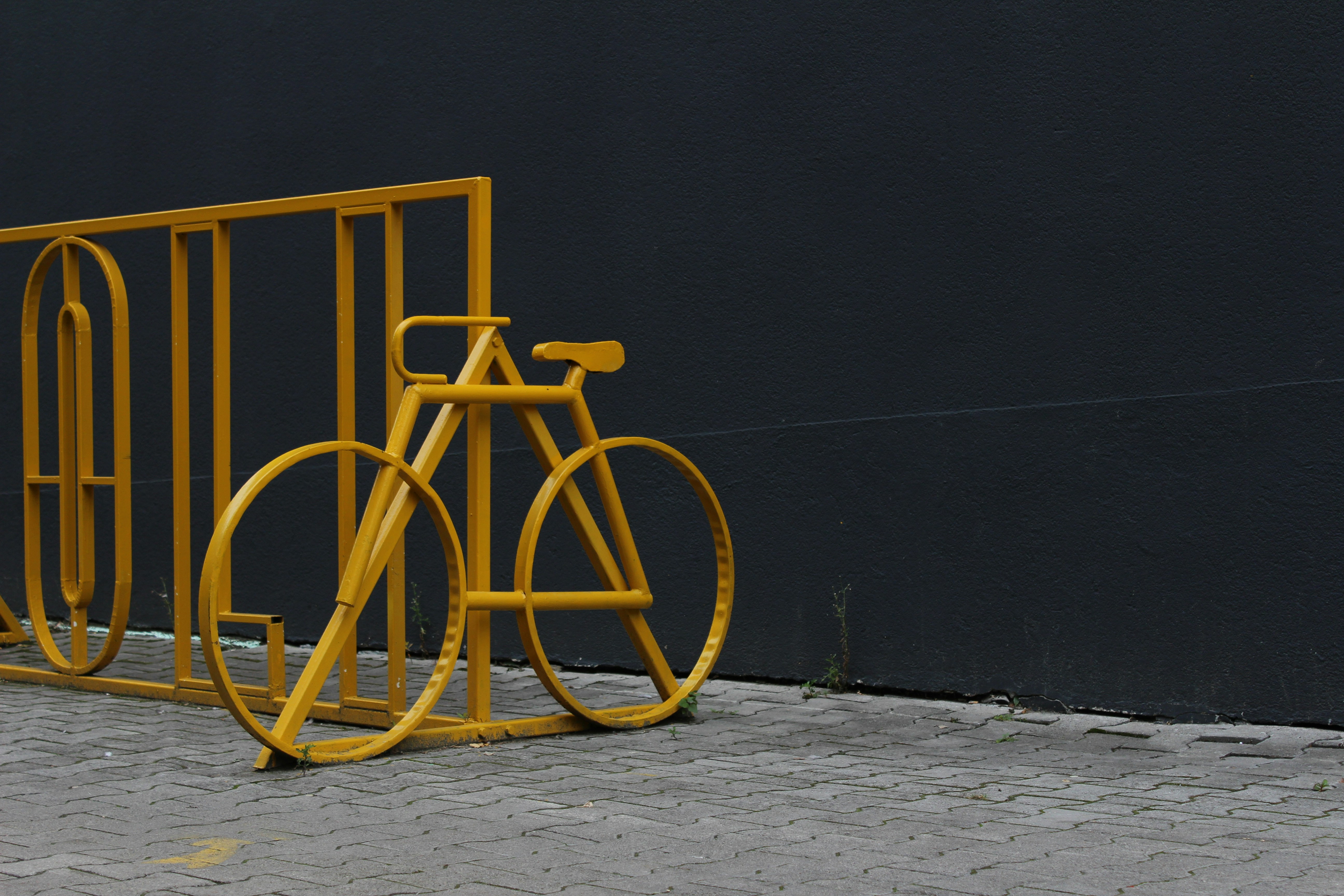 Yellow bicycle-shaped rack set against a dark wall on a concrete surface.