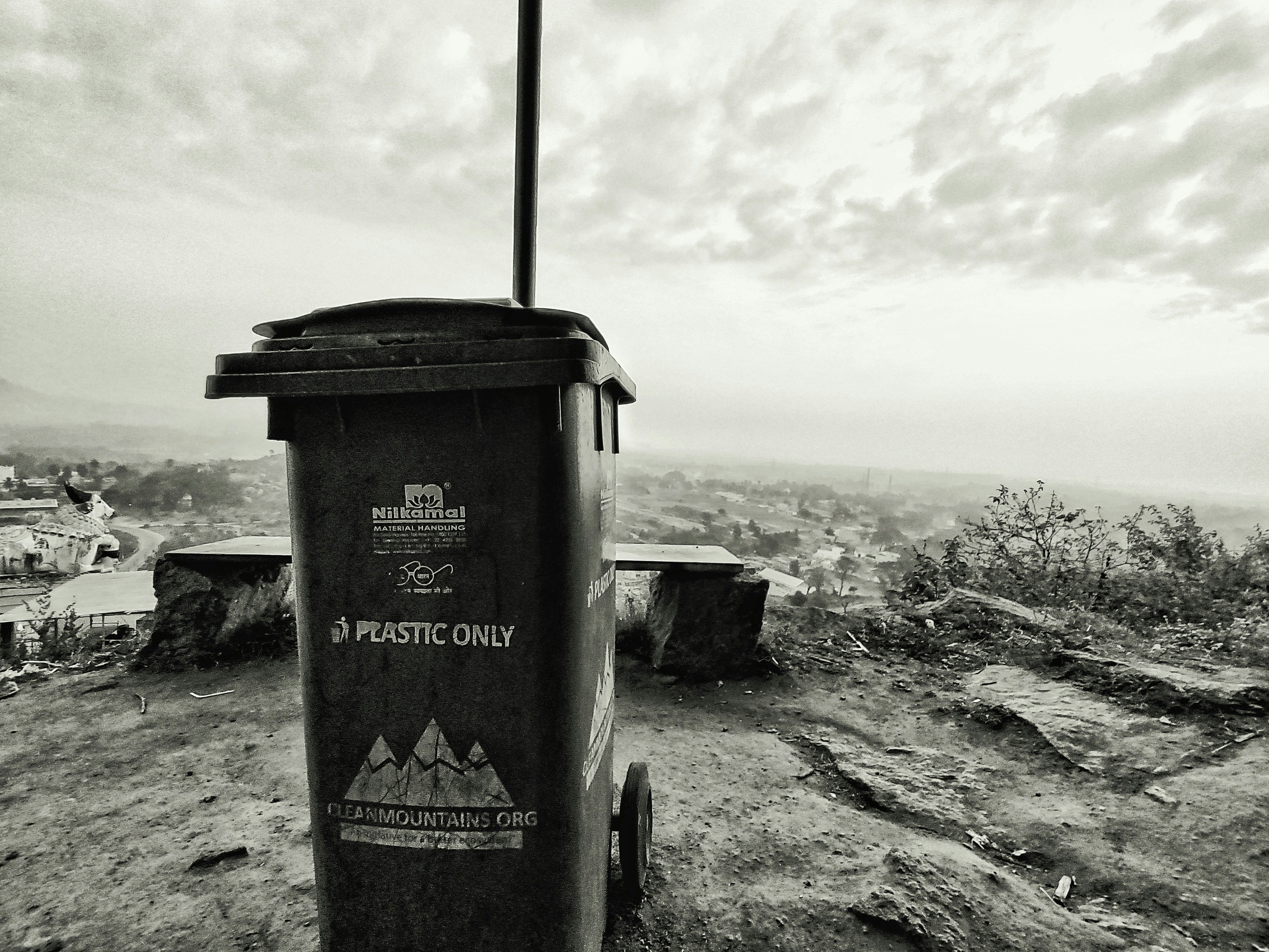 A black and white photograph of a recycling bin labeled 'PLASTIC ONLY' overlooking a scenic view, emphasizing environmental responsibility.