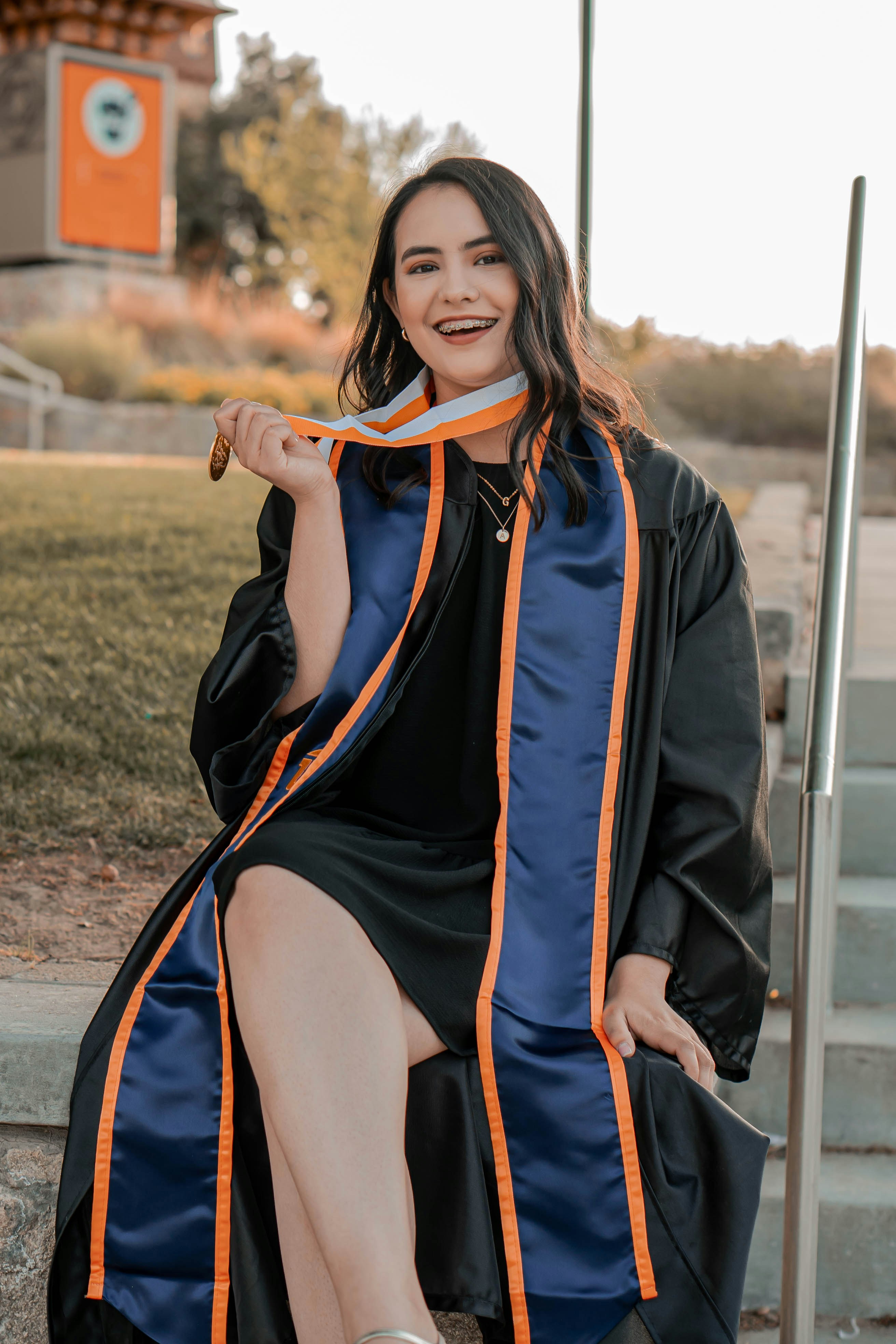 A woman in a graduation gown sitting on steps photo – Free University ...