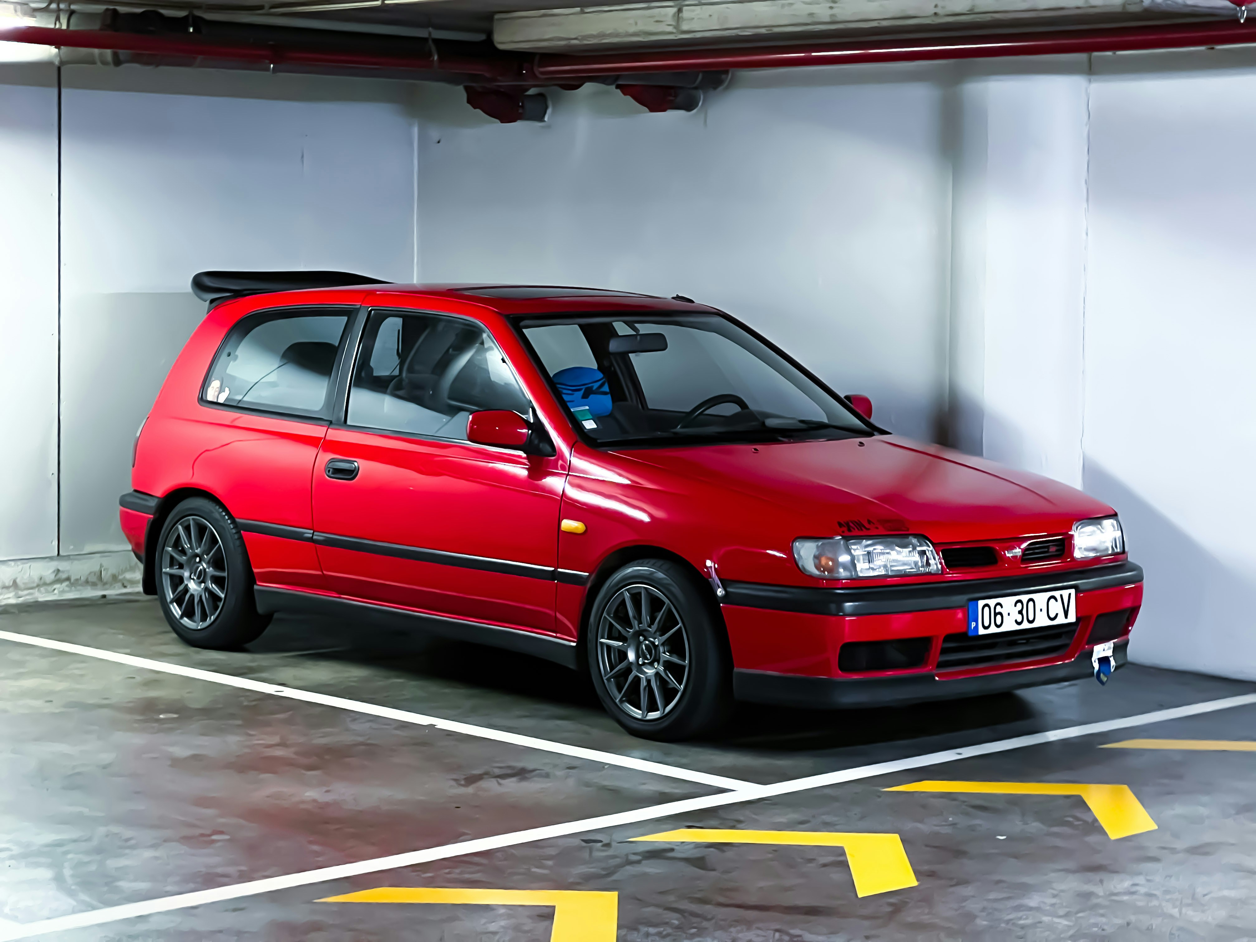 Red car parked in a dimly lit parking garage with yellow floor markings.