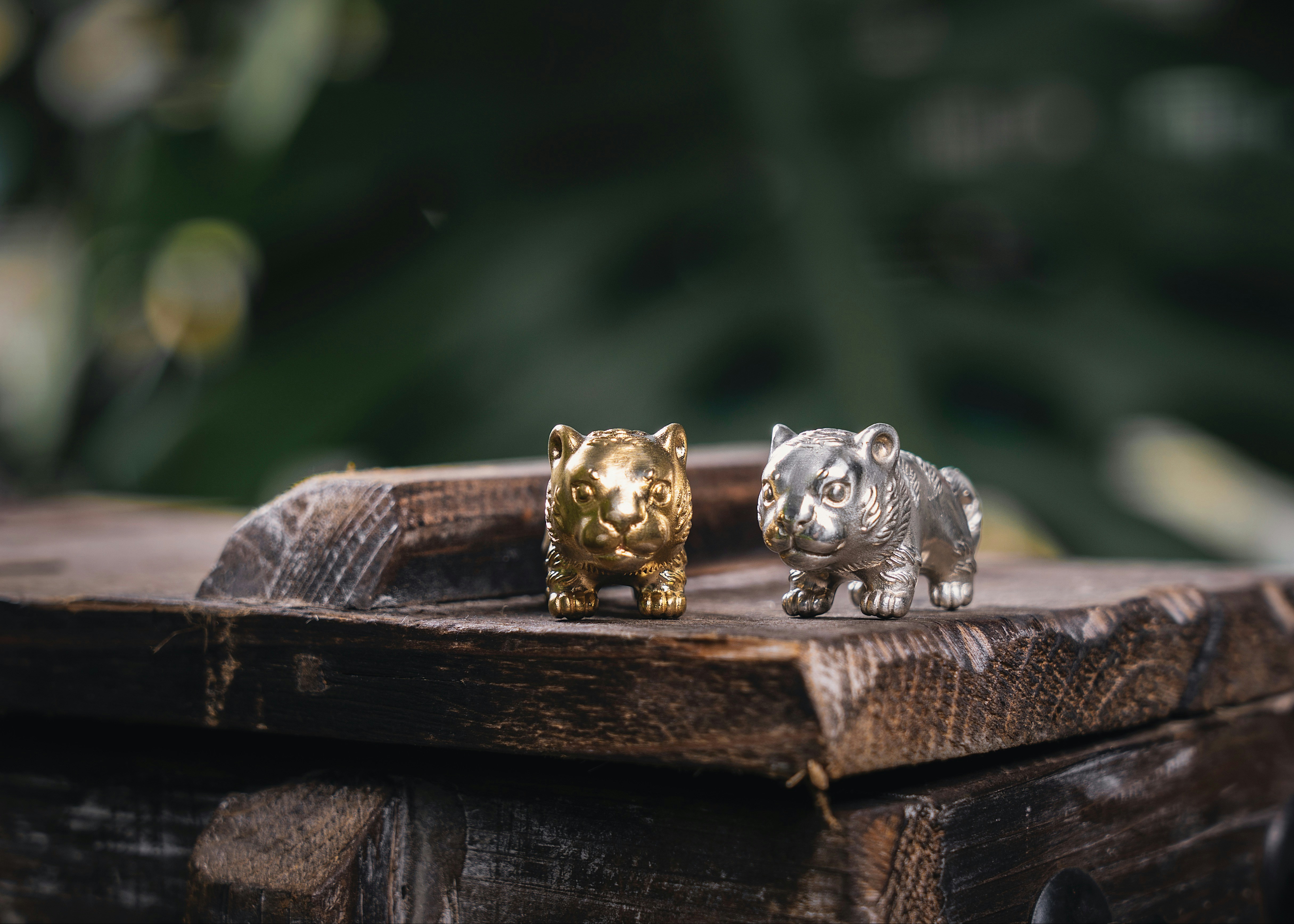Two small gold and silver tiger figurines sitting on top of a wooden ...