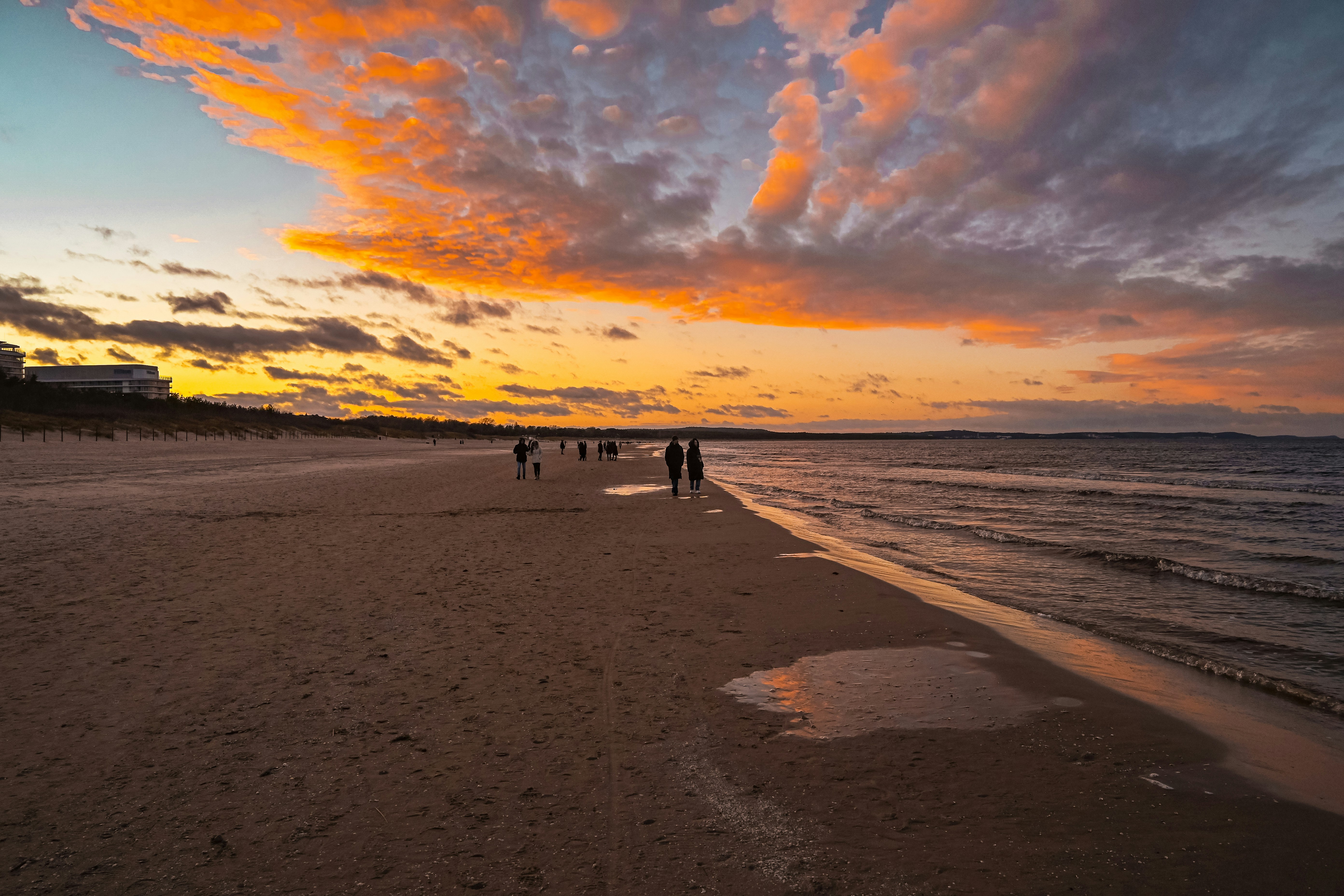 Vibrant sunset over a tranquil beach with silhouetted figures along the shoreline.
